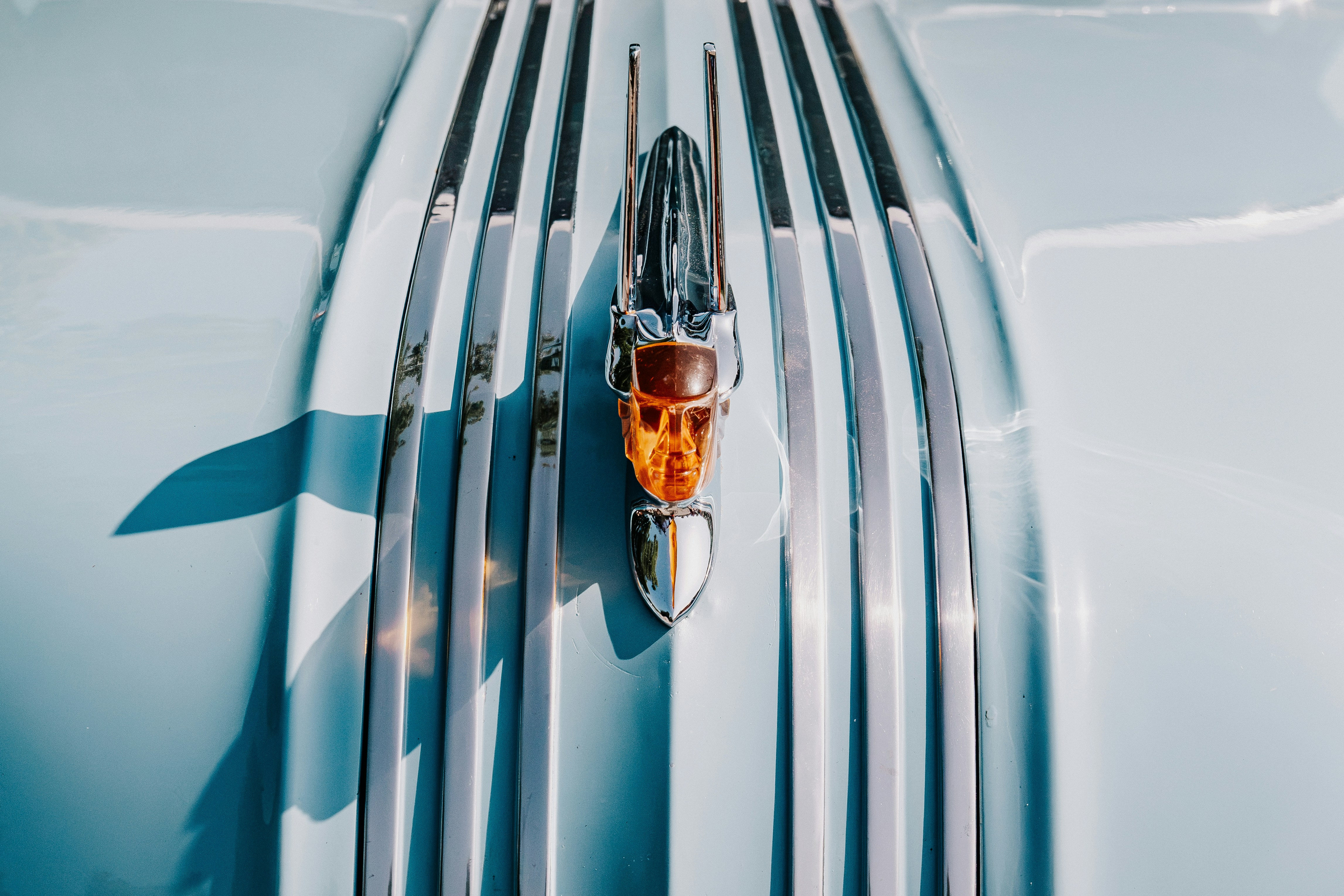 Chrome Crest: A Vintage Hood Ornament Reflected in Soft Seas of Blue