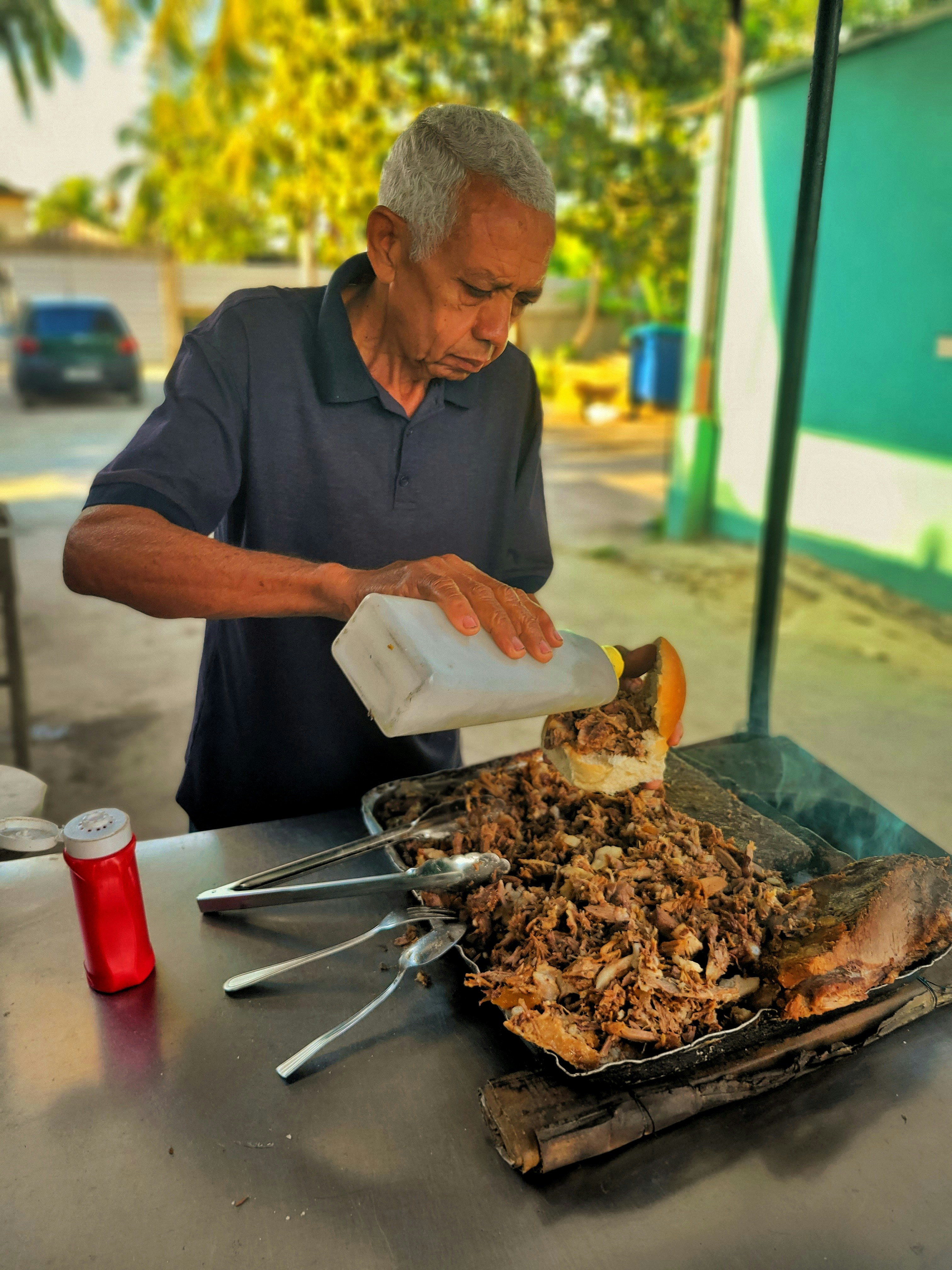 A street food vendor preparing a traditional Cuban pork sandwich at a small roadside stall.