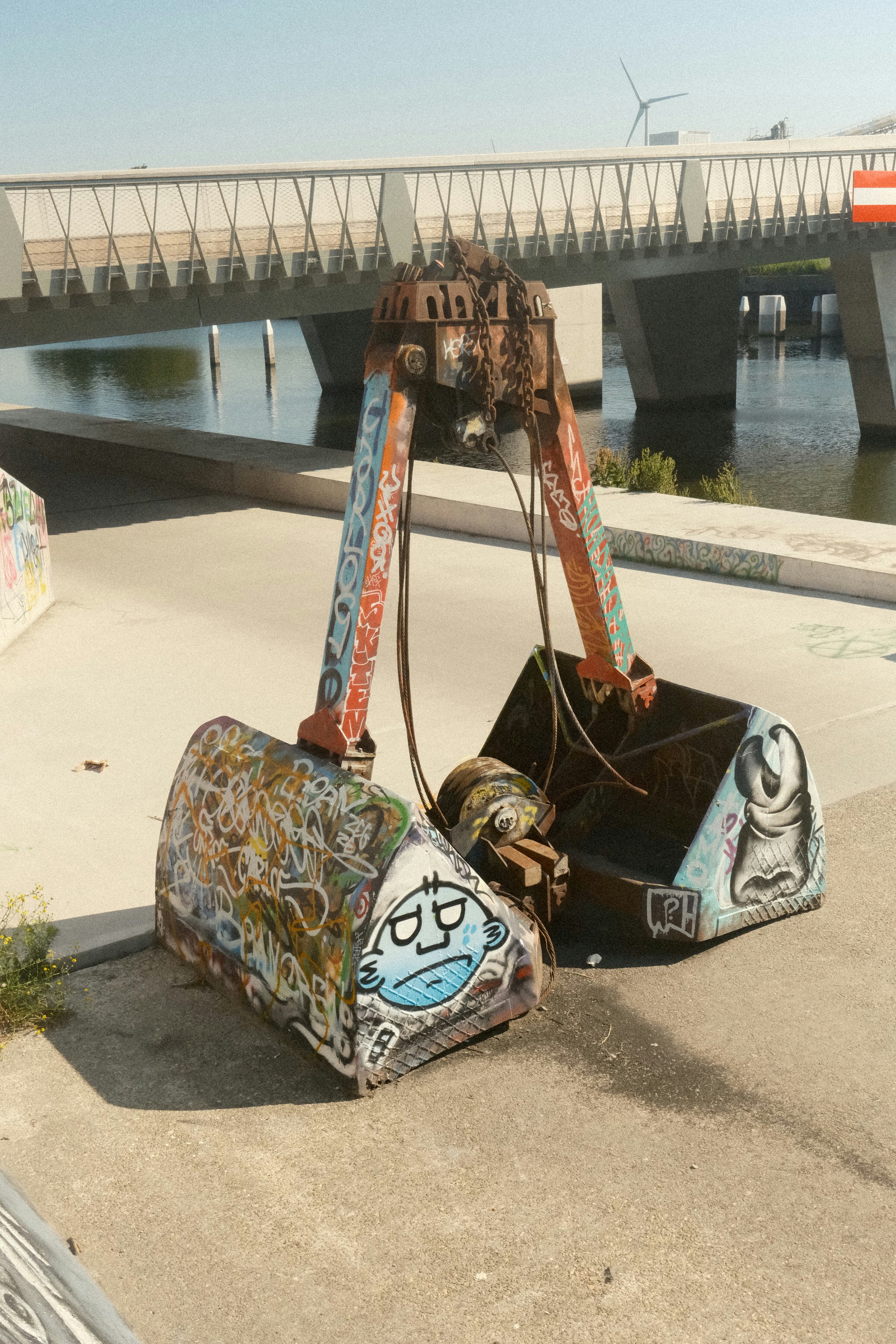 Graffiti Bucket Cranes by the River Under a Modern Bridge