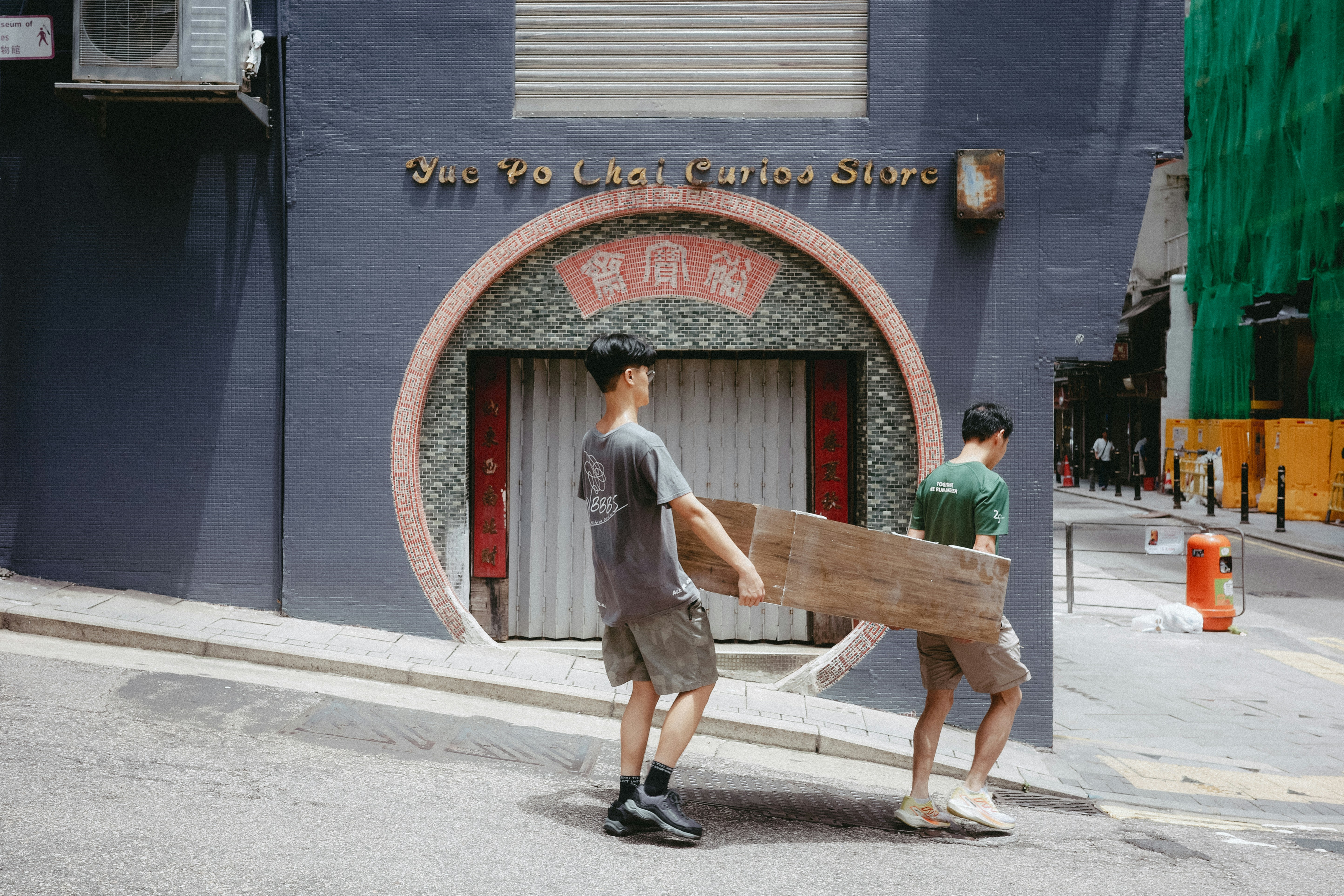 Two Helpers in a Neon-Circled Shopfront Carry a Wooden Burden