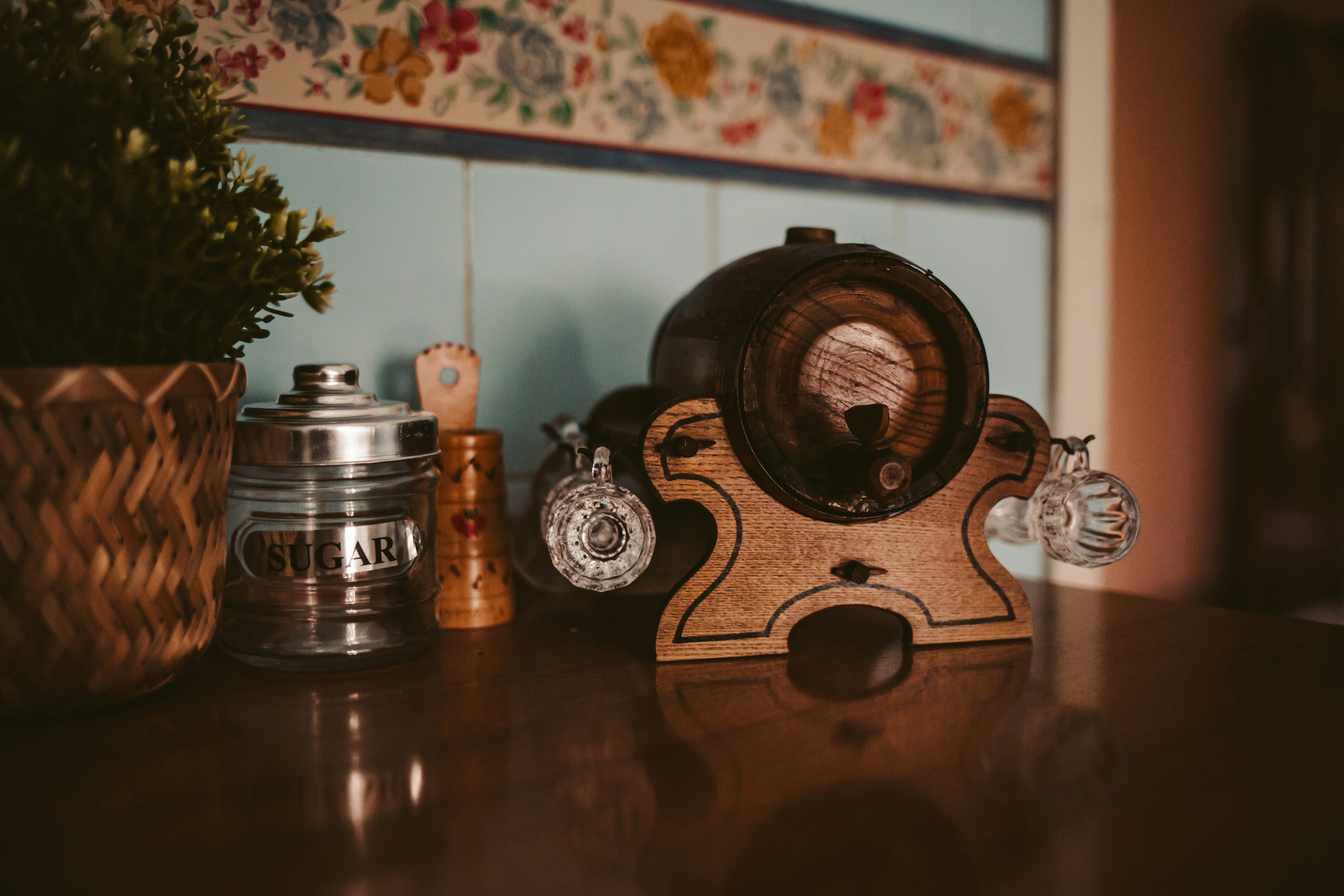 Decorative wooden barrel dispenser, glasses, and plant on a table.