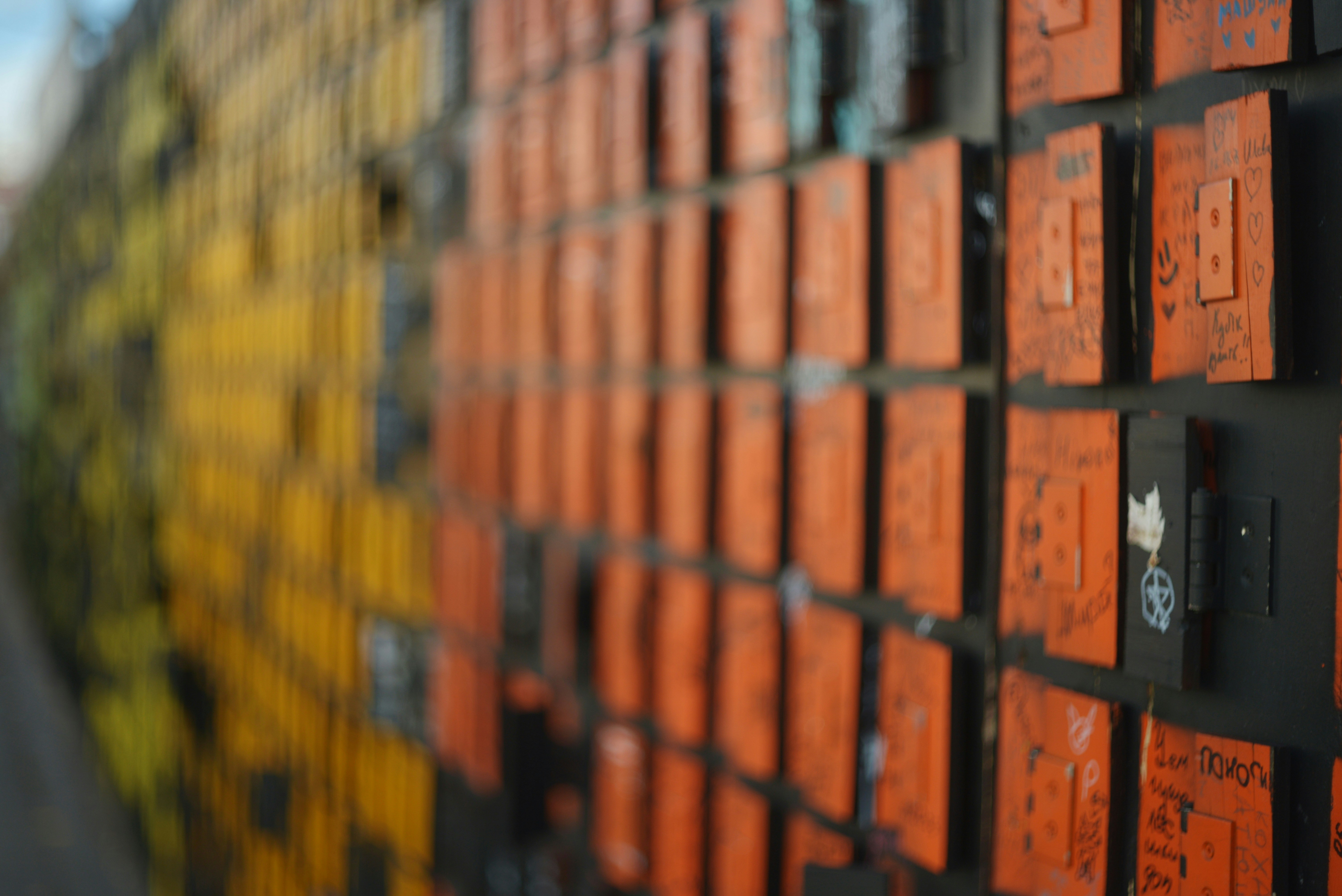 Close-up of a wall covered with colorful, stacked rectangular tiles or tags in orange, yellow, and dark tones; shallow depth of field softens the background, highlighting texture and graffiti-like markings.