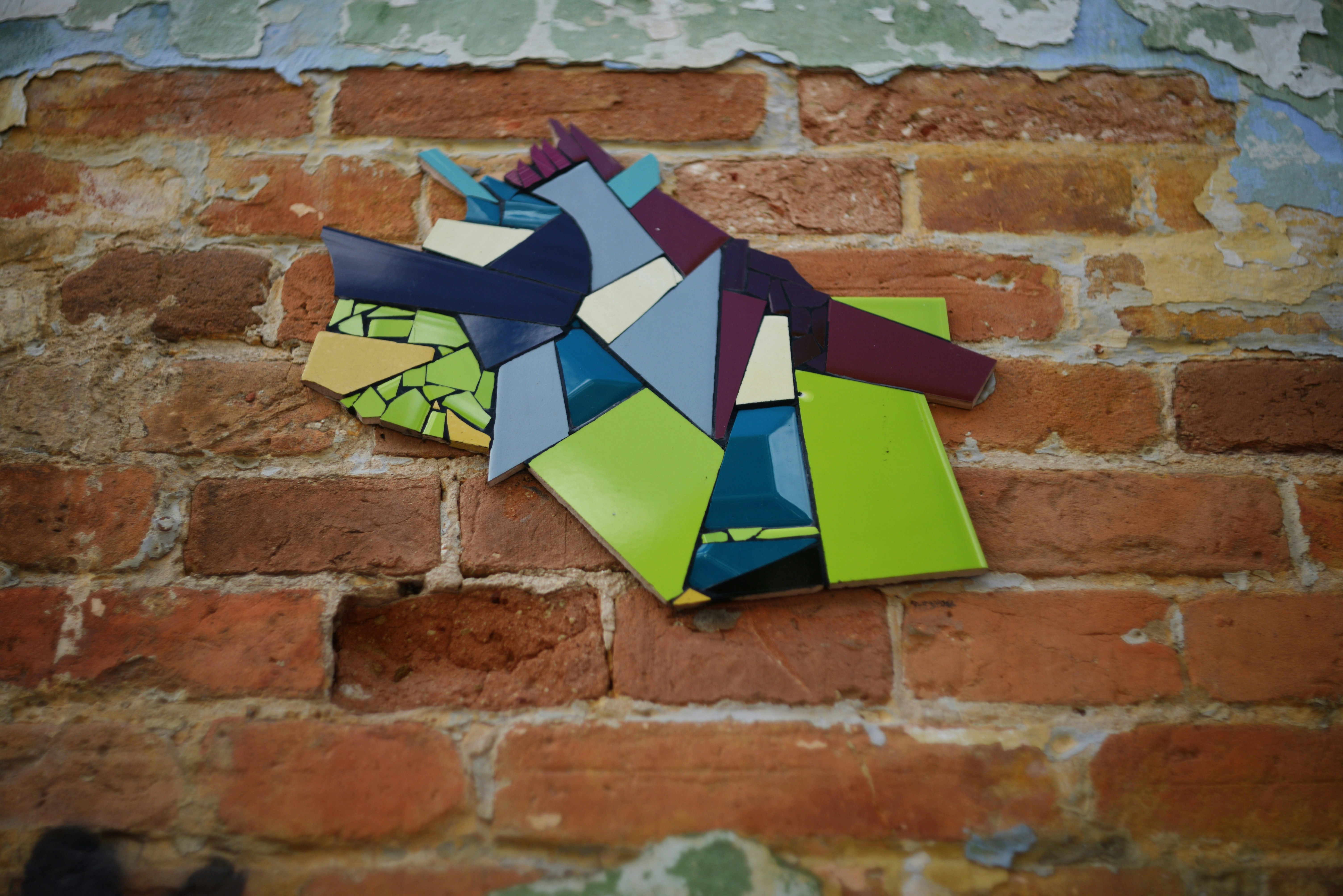 Colorful geometric shapes arranged on a weathered brick wall, creating a tactile collage feel against textured mortar.