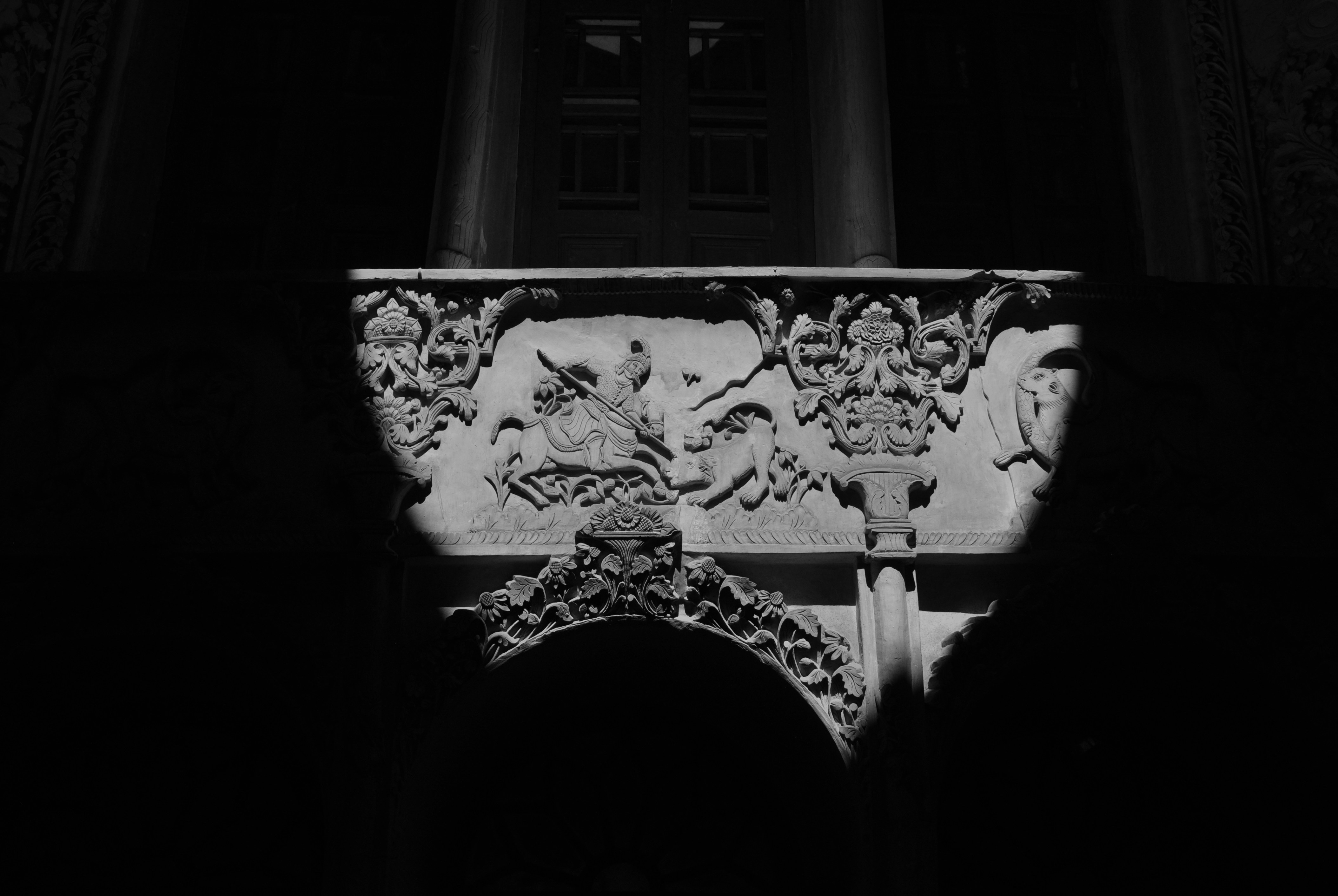 Dramatic Light on Historic Persian Stone Relief in Kashan A fine art black-and-white photograph showcasing dramatic natural light illuminating an intricate Persian stone relief on a historic building in Kashan, Iran. The detailed architectural carvings, timeless craftsmanship, and strong contrast create a striking visual representation of Iranian cultural heritage and traditional Persian architecture. Perfect for architecture, history, culture, travel, editorial, and fine art projects.