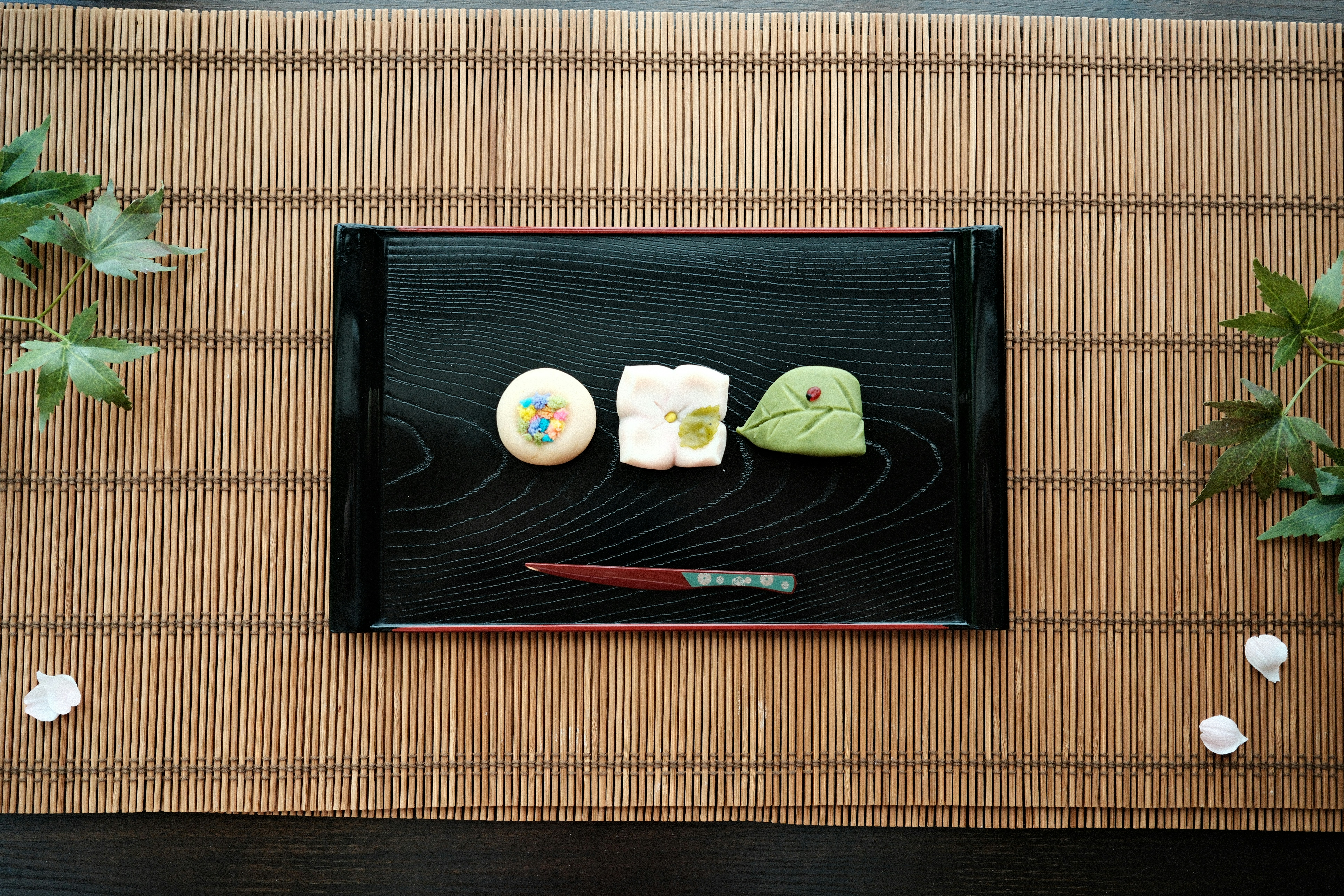 Three japanese sweets and a stick on a black tray.