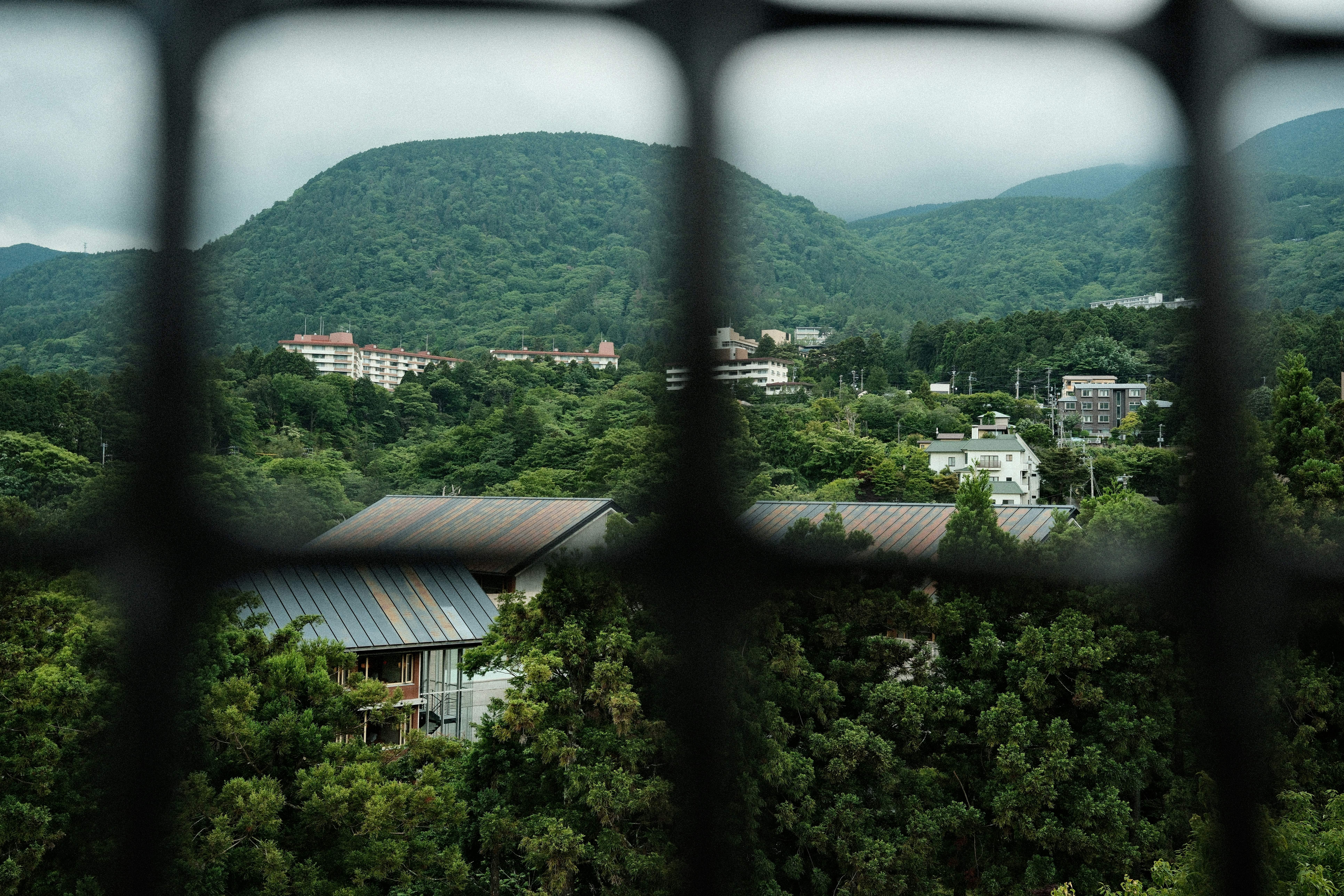 Distant hillside town framed by dark window bars, with a green valley and layered mountains in the background.
