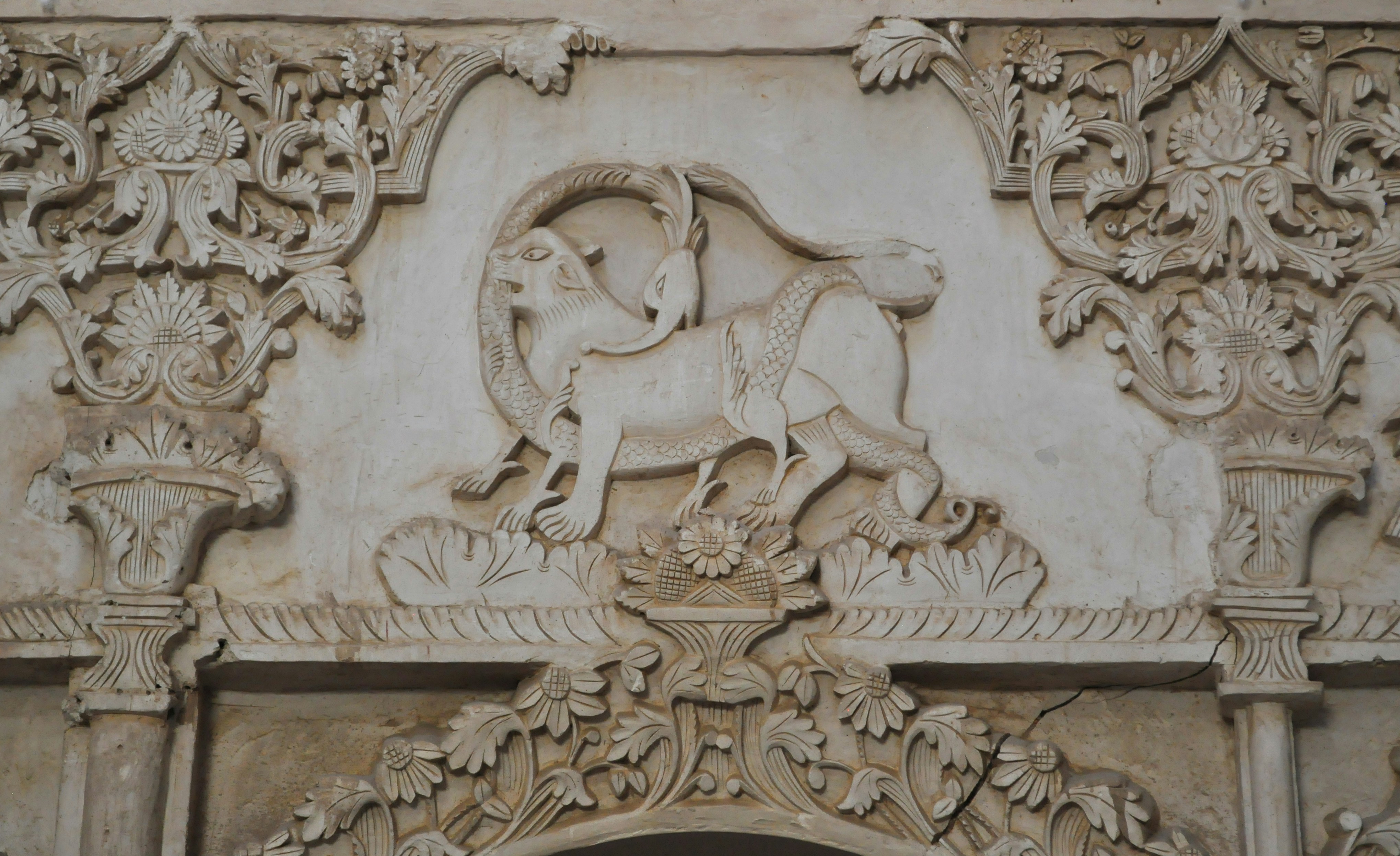 A detailed architectural photograph capturing a beautifully carved mythical winged lion relief surrounded by elegant floral ornaments on a historic building in Kashan, Iran. This image showcases the richness of Persian architectural decoration, traditional craftsmanship, and Iranian cultural heritage. Ideal for architecture, travel, history, editorial, and fine art projects. Photo by Hedishka | Hediyeh Hedayati