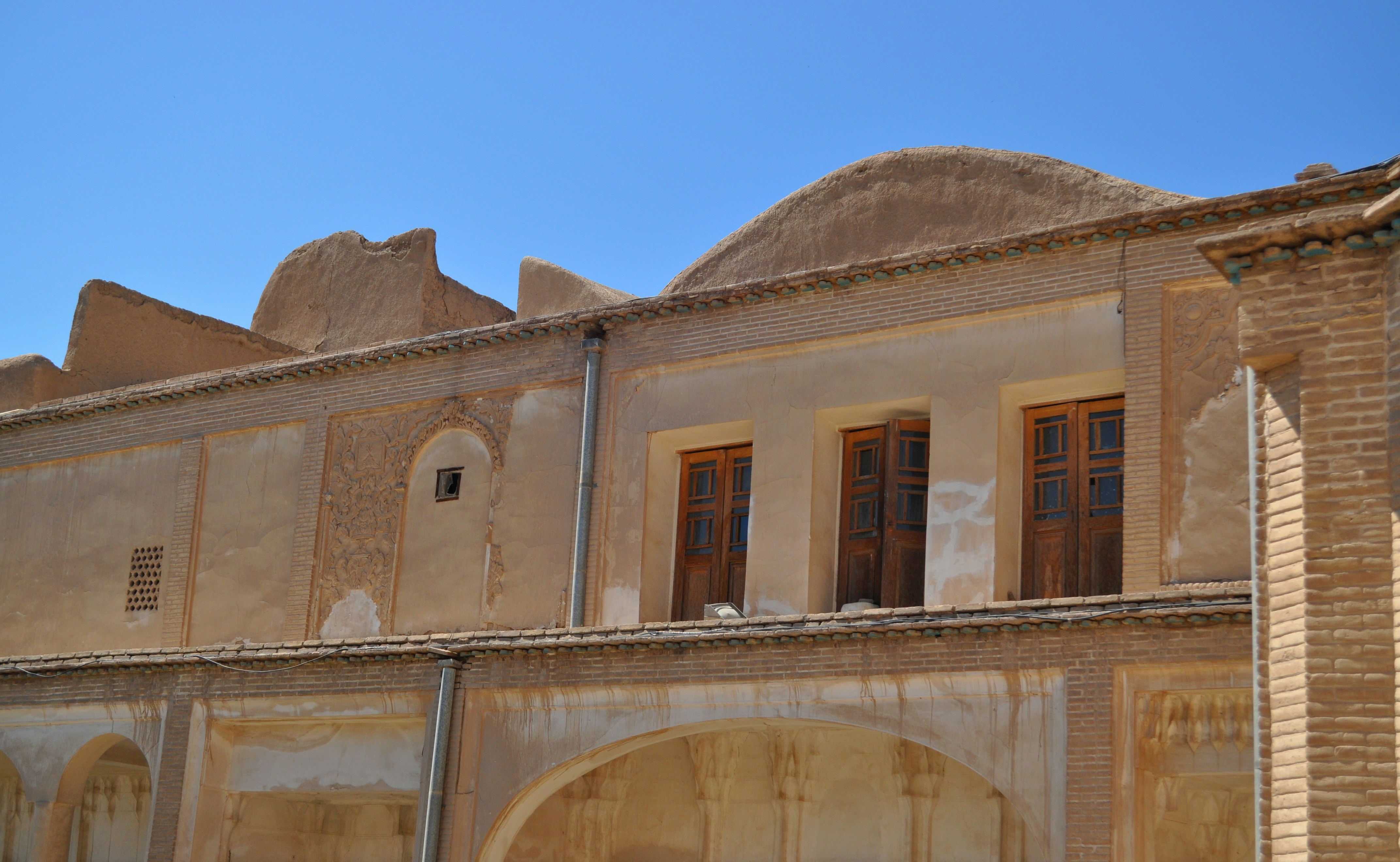 A high-resolution architectural photograph of a historic Persian house in Kashan, Iran. The image showcases traditional adobe architecture, handcrafted brickwork, elegant wooden windows, and distinctive domed roofs that reflect the timeless beauty of Iranian heritage. Perfect for travel, architecture, cultural heritage, editorial, tourism, and design projects. Photo by Hedishka | Hediyeh Hedayati
