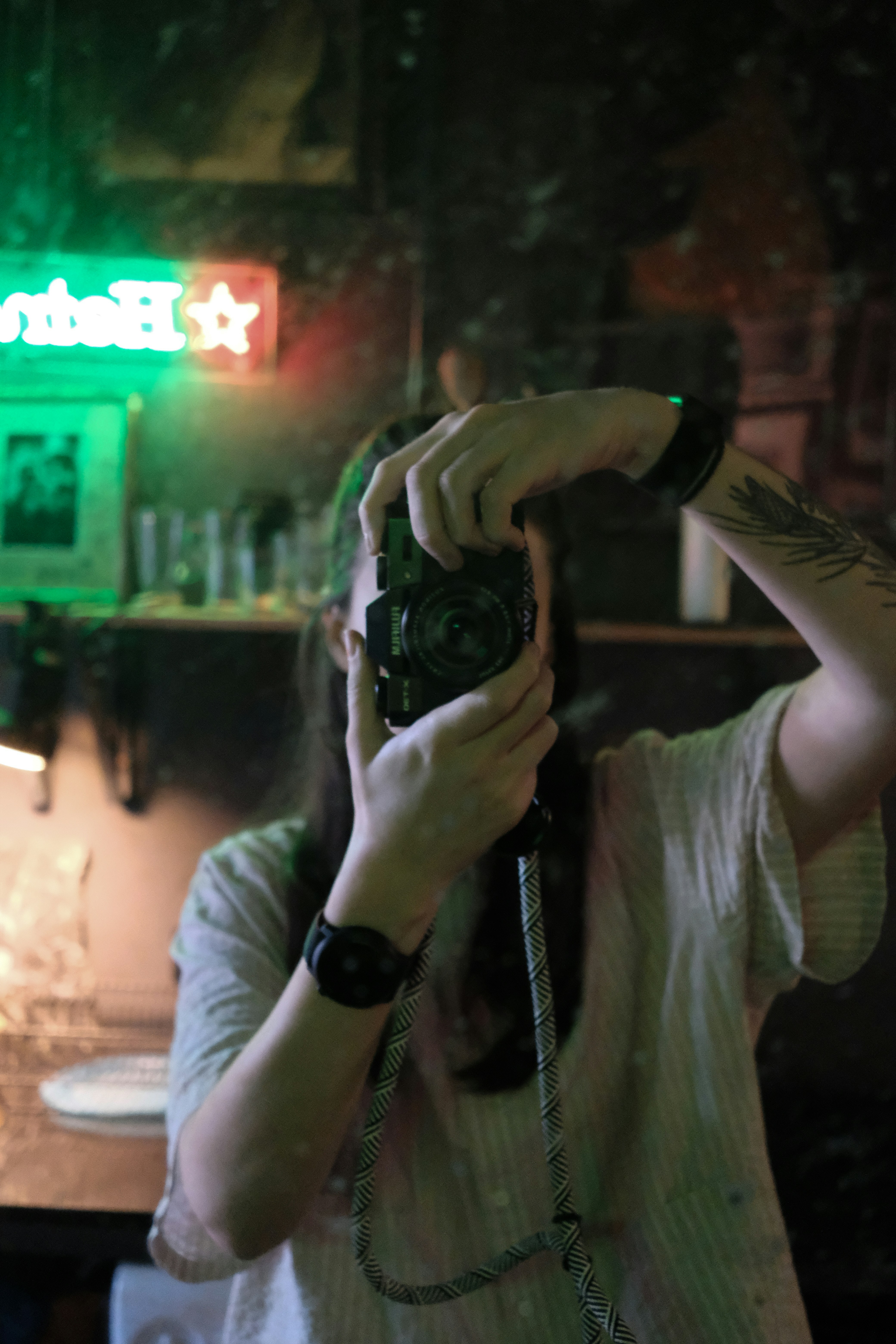 Person taking a mirror selfie with a camera, neon background.