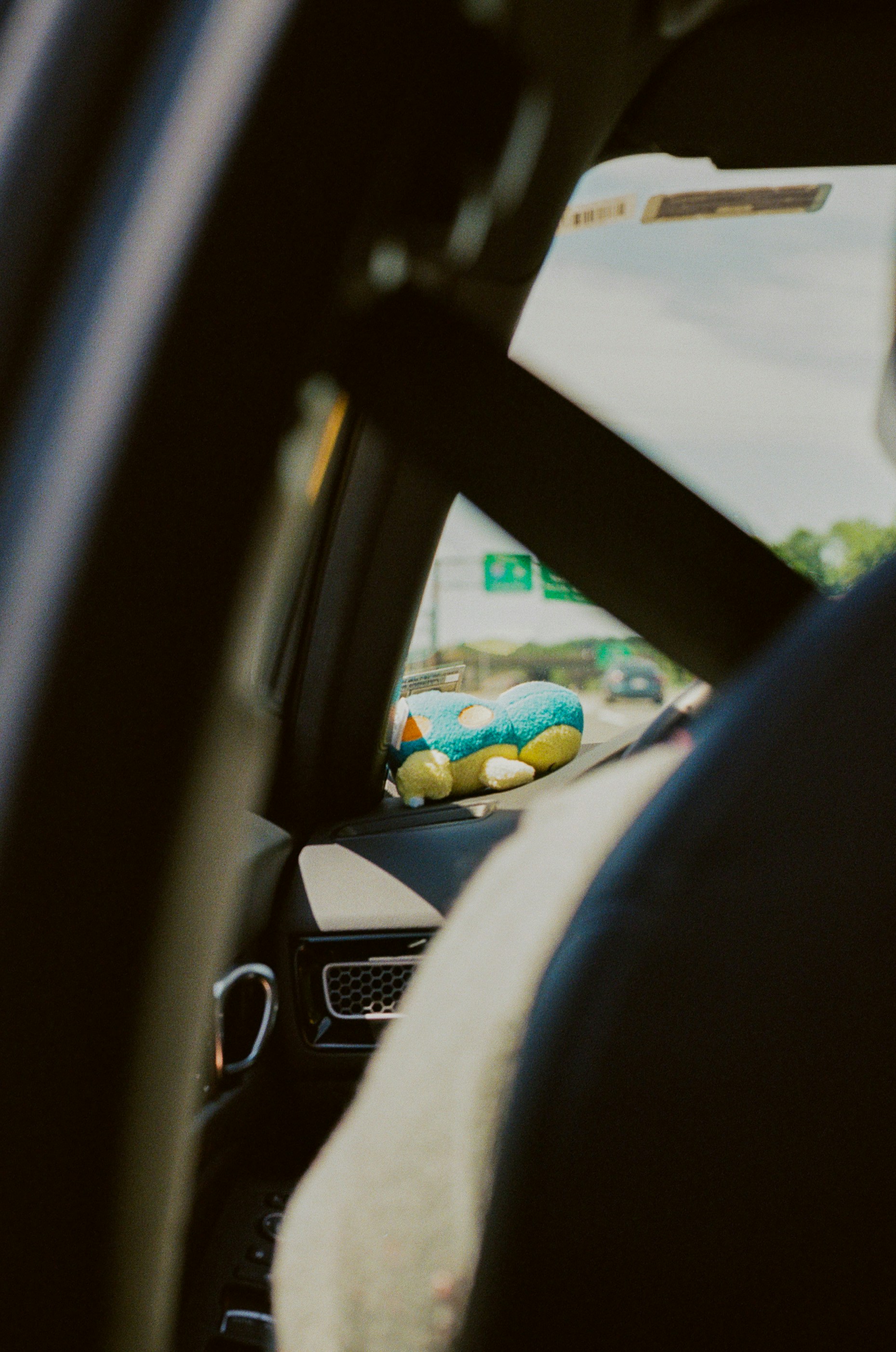 A small plush toy reflected in a car mirror during a road trip, captured on film with a quiet nostalgic feeling.