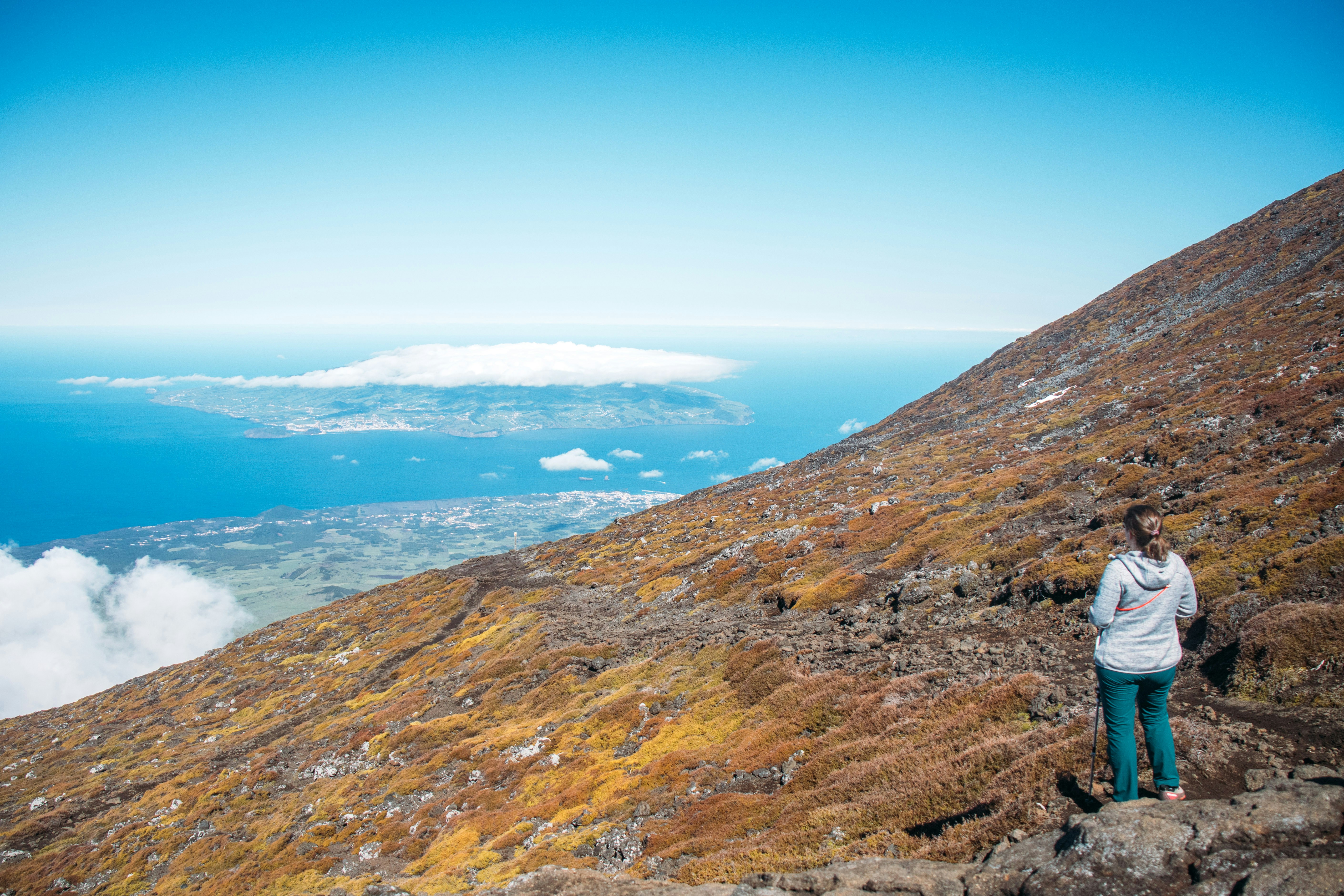 Cliffside Horizon: A lone hiker on a sunlit volcanic slope gazes toward the distant sea