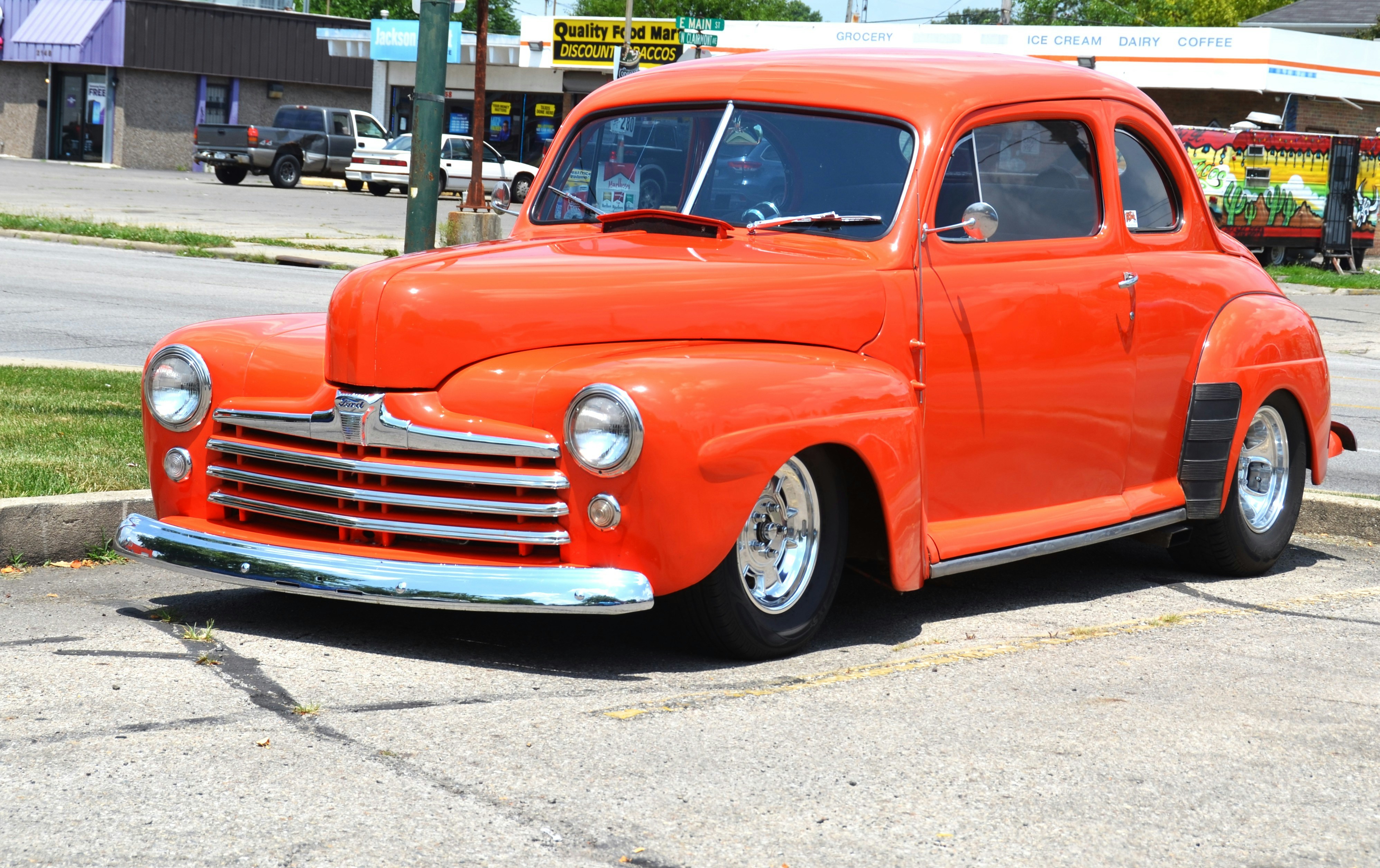 Orange vintage sedan crowned by chrome grill in a sunlit lot
