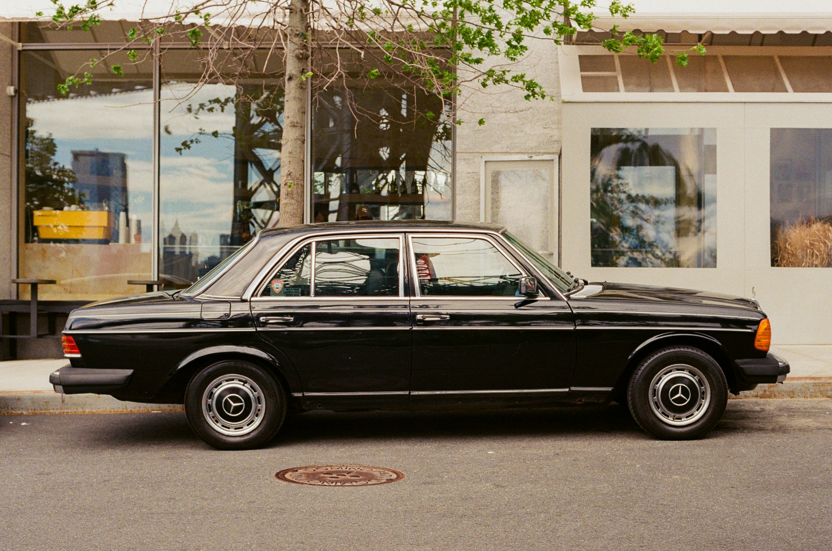 A classic black Mercedes parked on a quiet city street, captured on film with a timeless vintage atmosphere.