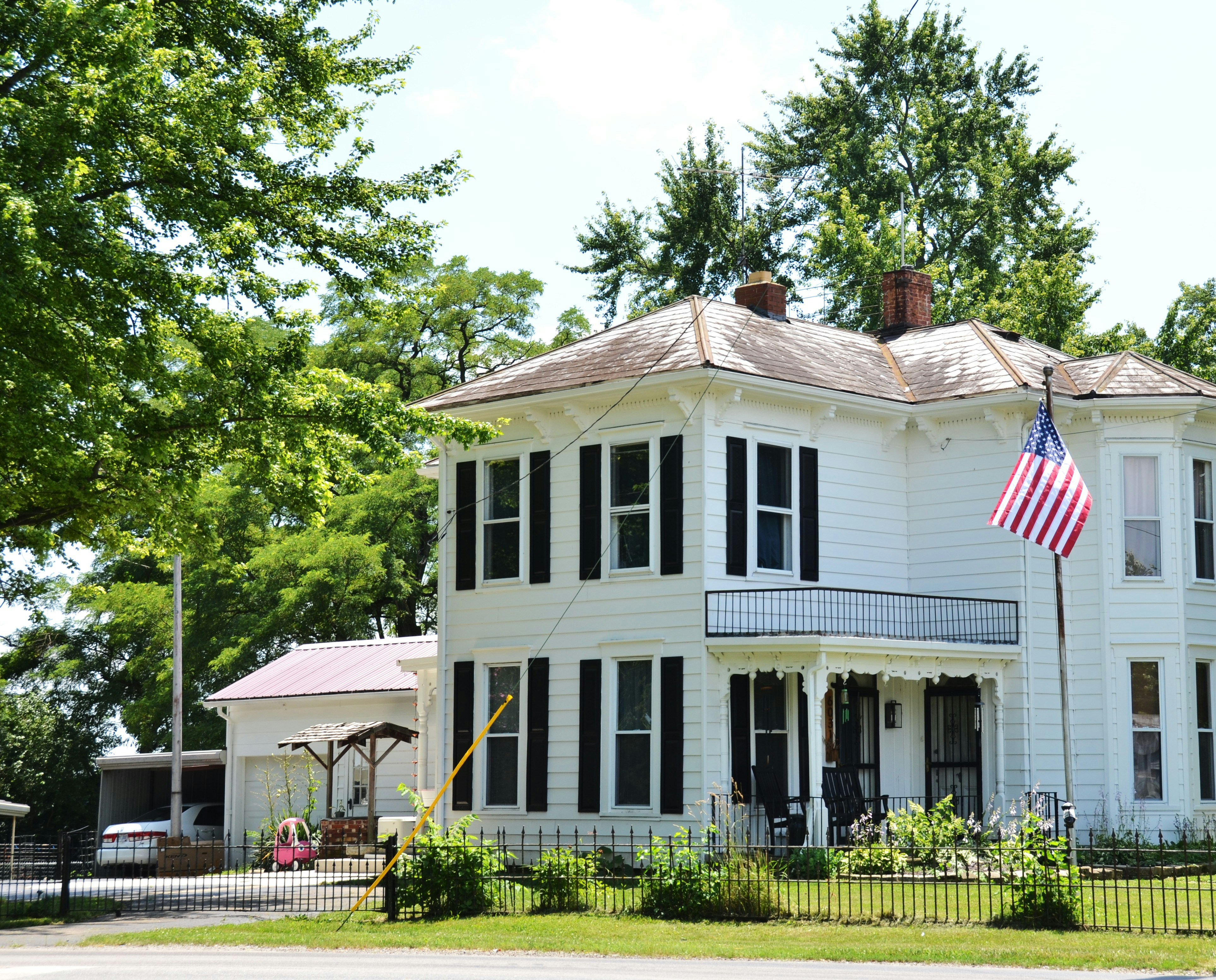 White Victorian House with American Flag Under a Sunlit Canopy