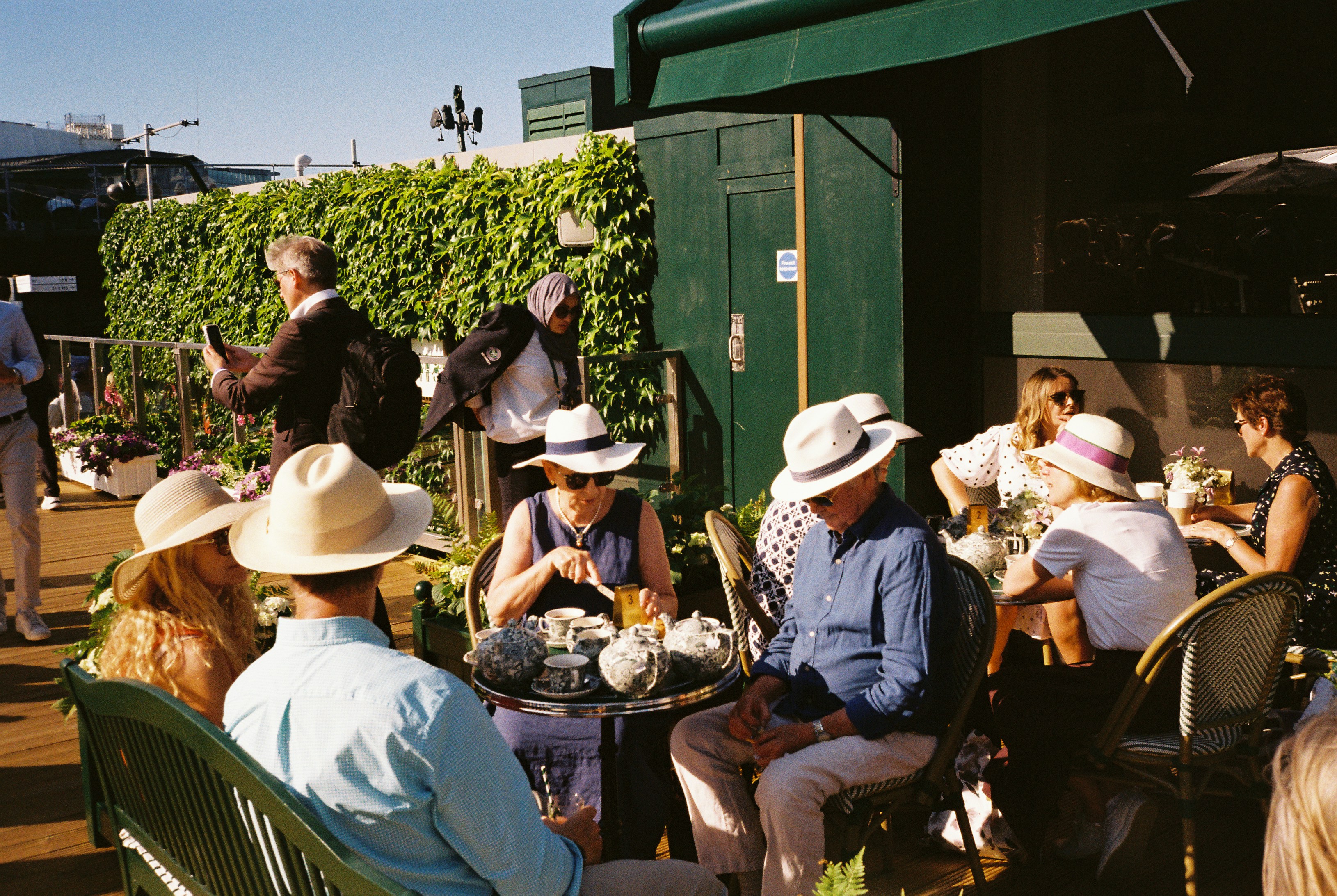 Sunlit Terrace Mosaic: People in Hats Sharing a Meal under Greenery