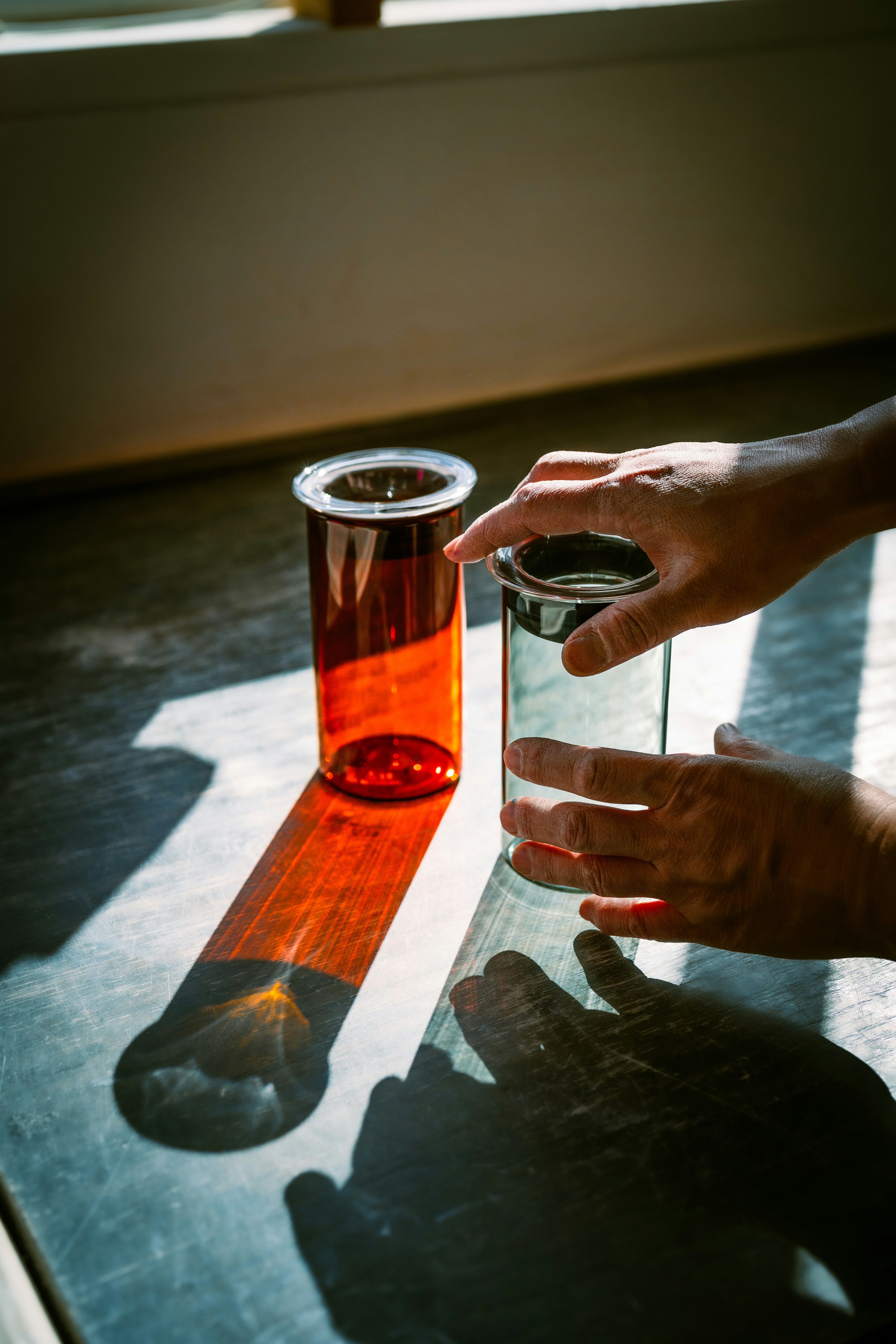 Hands with Glasses Casting Long Shadows Over a Sunlit Table