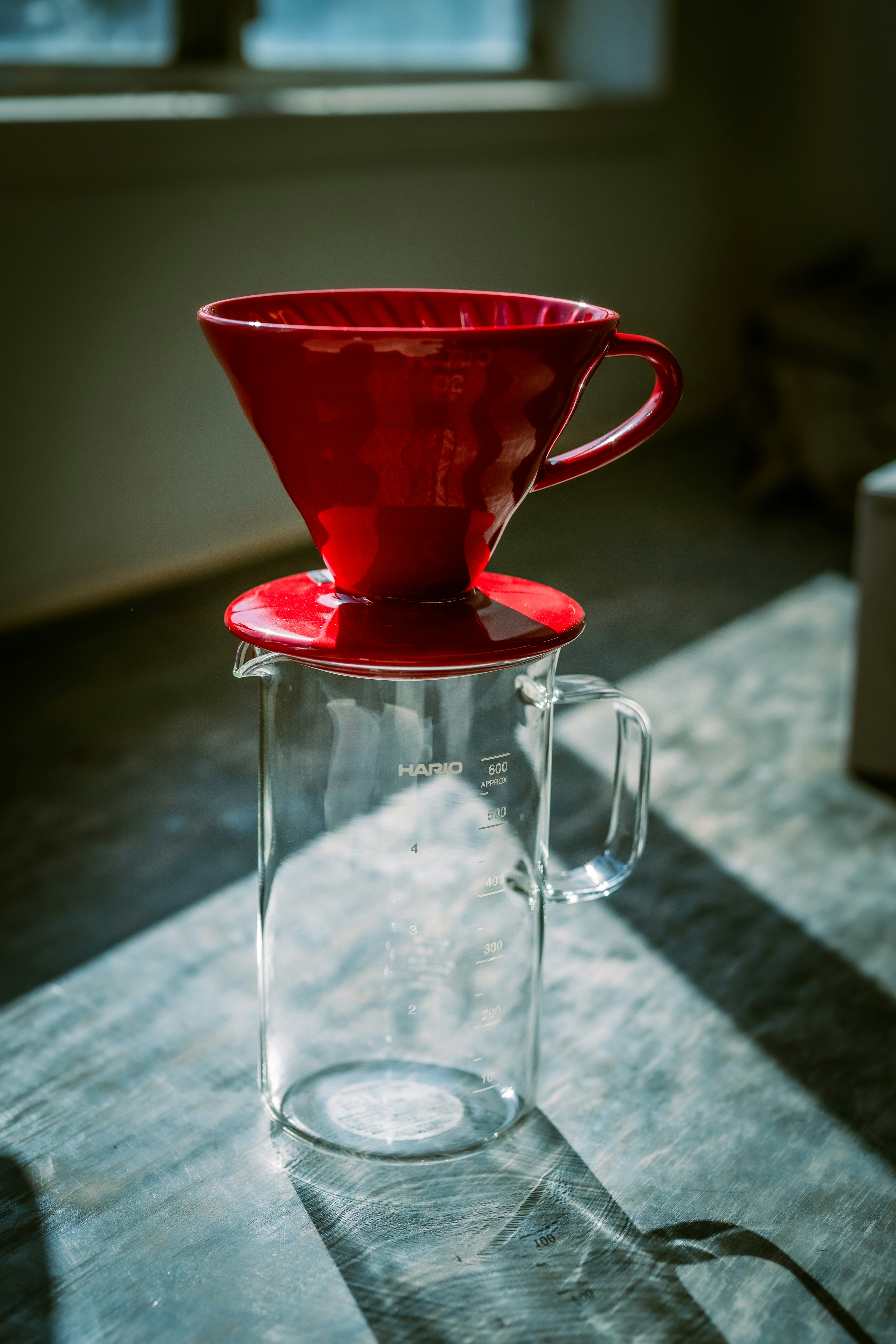 Red pour-over coffee dripper on a glass carafe in sunlight.