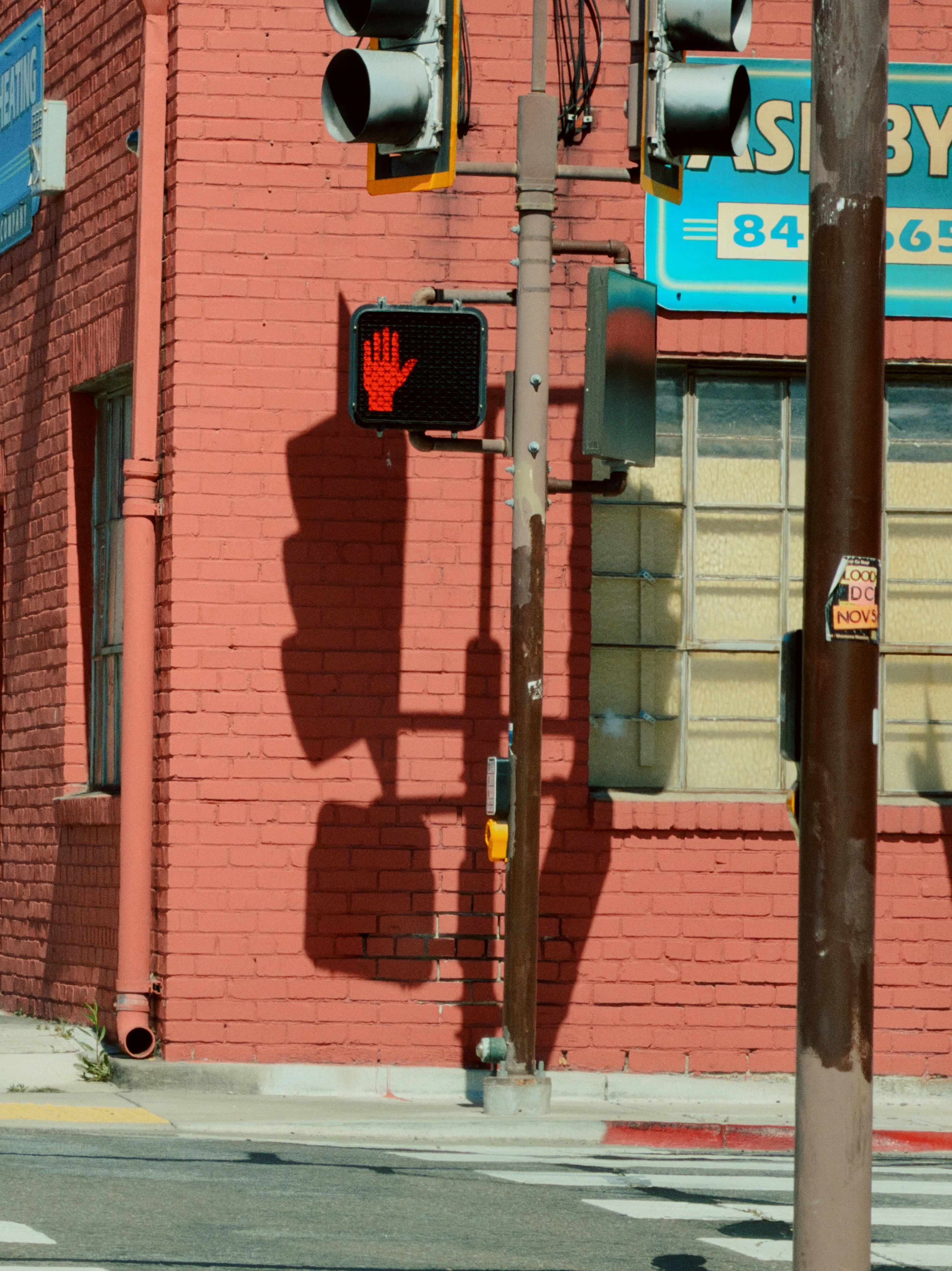 Shadowed Crosswalk: A Raised Hand Signal on Brick and Asphalt