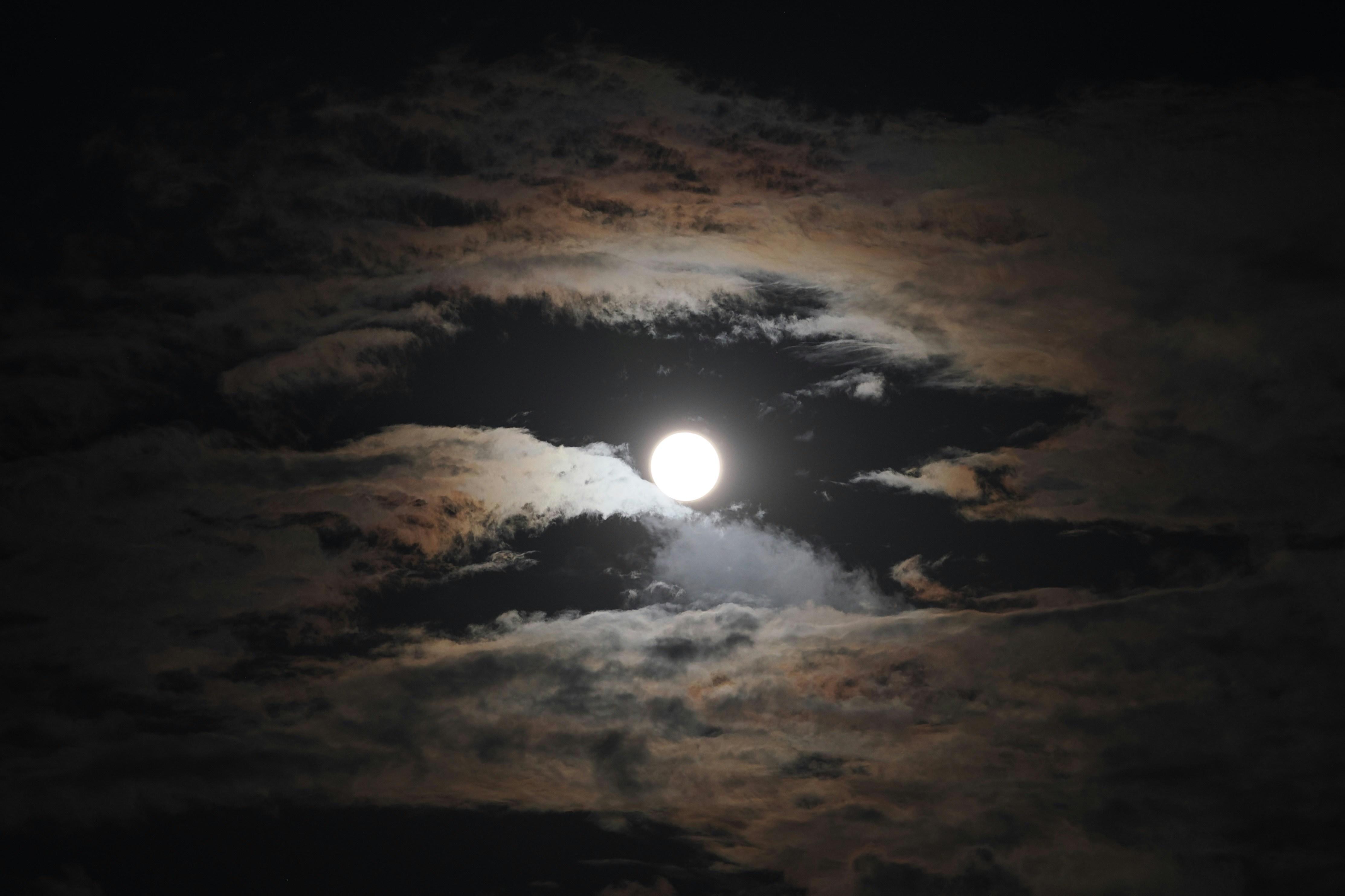 A bright full moon shines through dark, cloudy night sky.