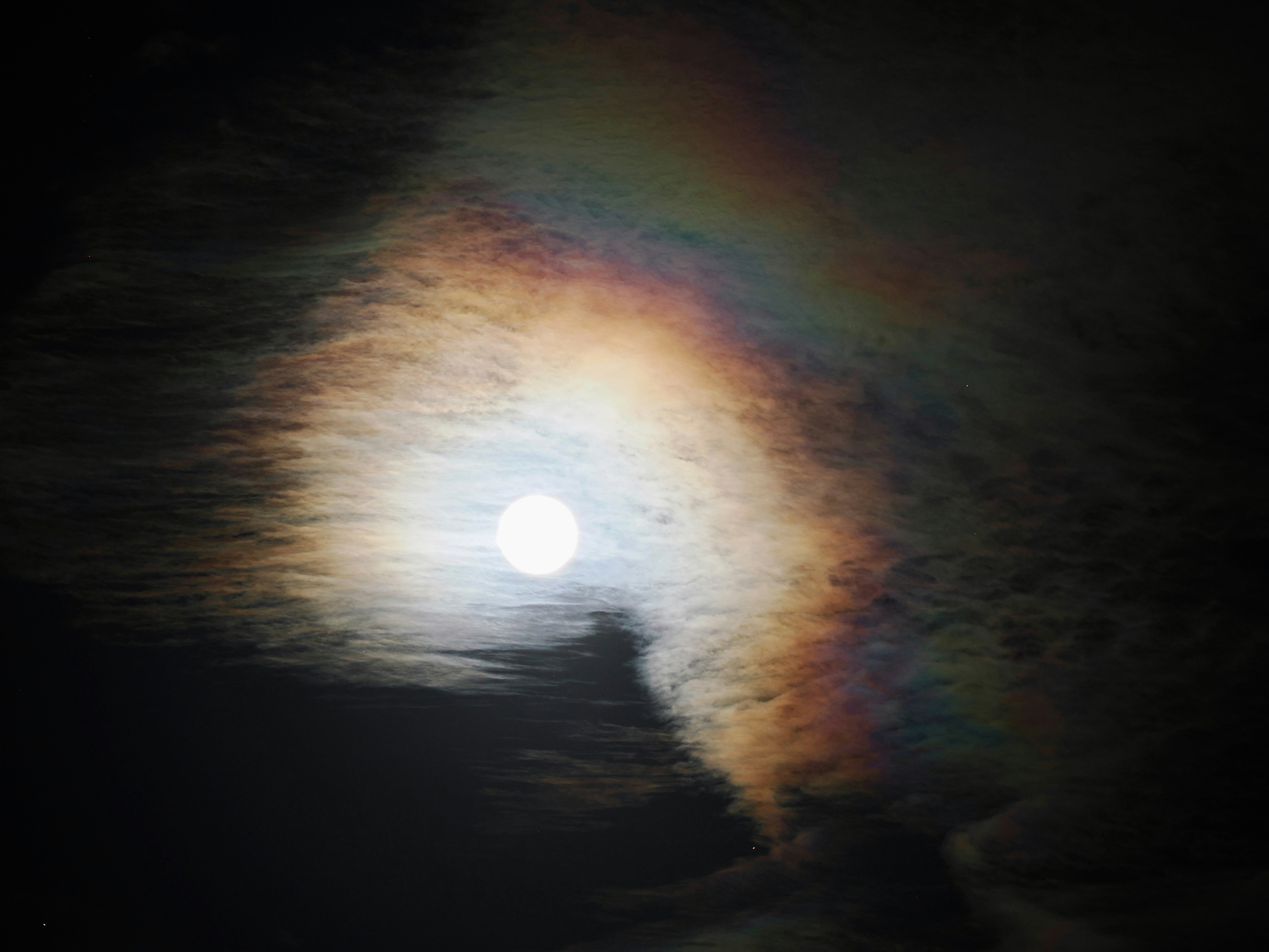 Bright moon with colorful iridescent clouds and a rainbow halo.