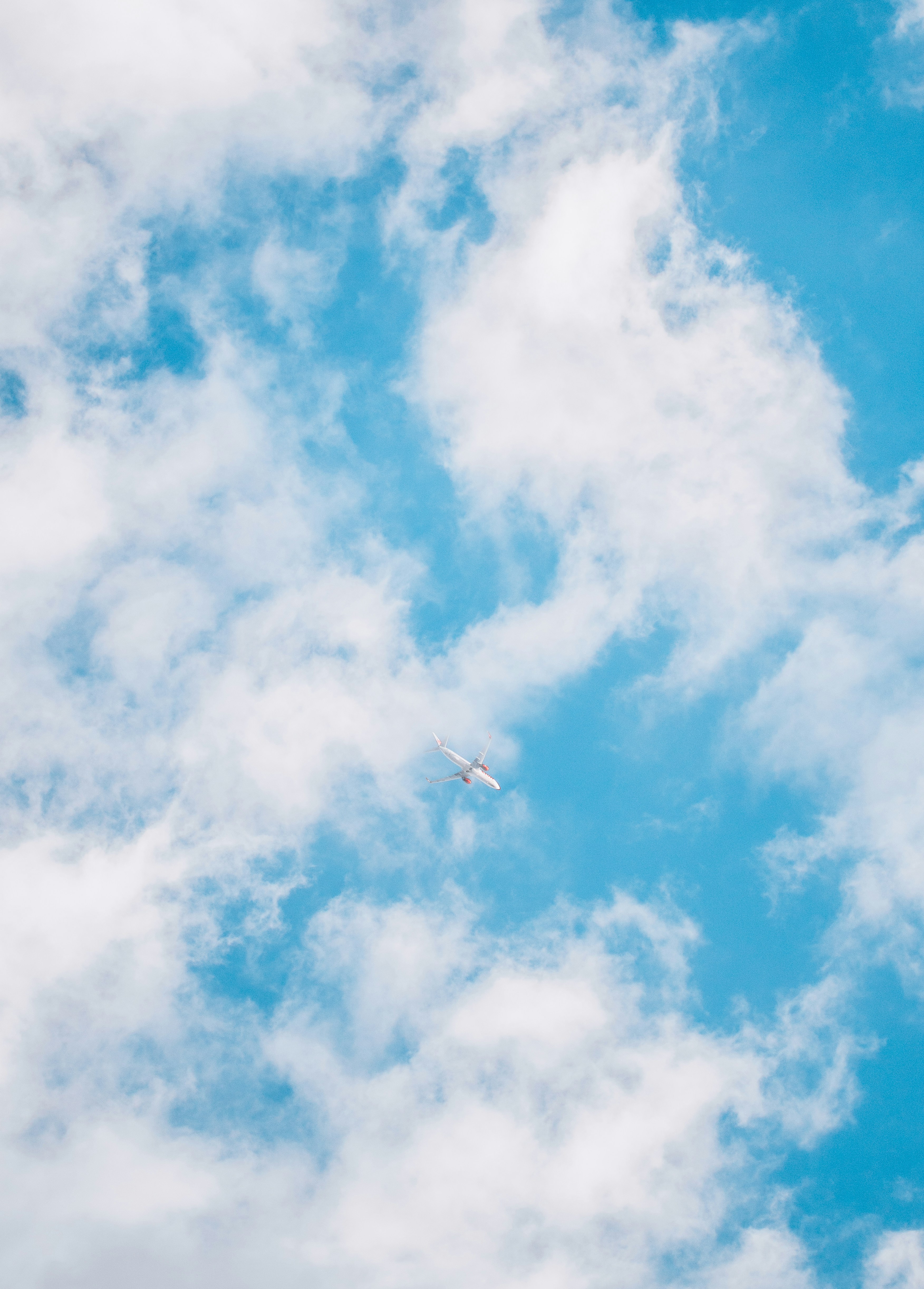 A small airplane flies through a bright blue sky dotted with fluffy white clouds, captured from below to emphasize height and openness. (Logos/illustration status: photograph).