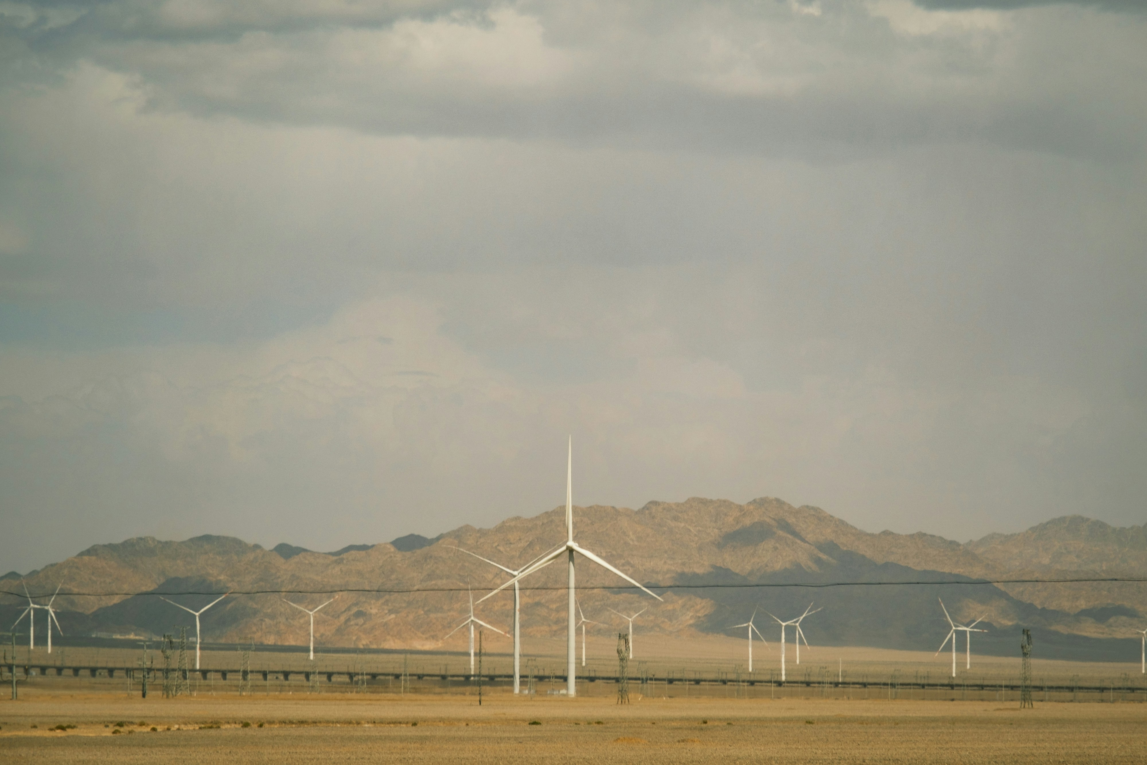 White wind turbines against mountains under a cloudy sky.