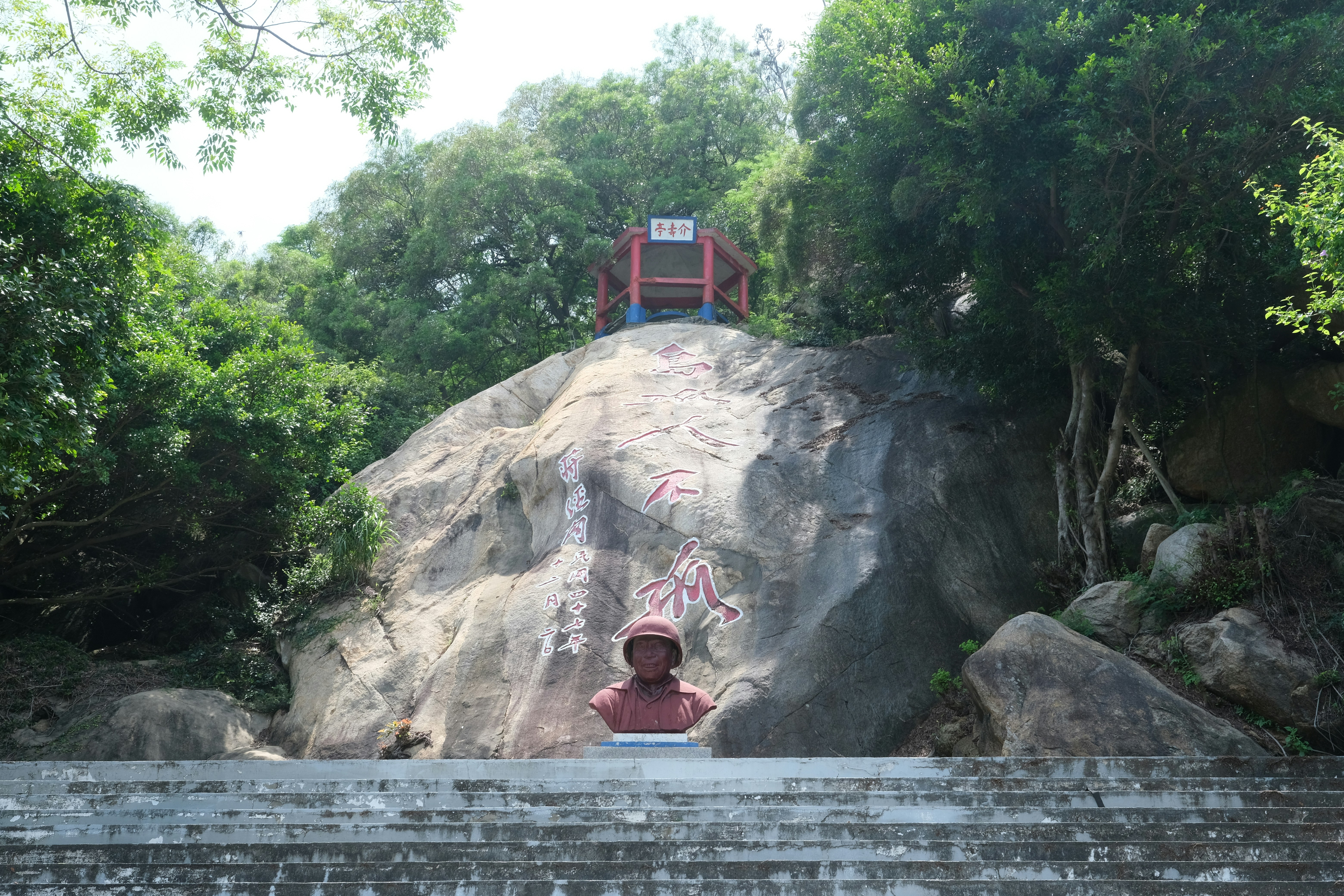 Person at the base of a rocky hill with a red overlook platform above