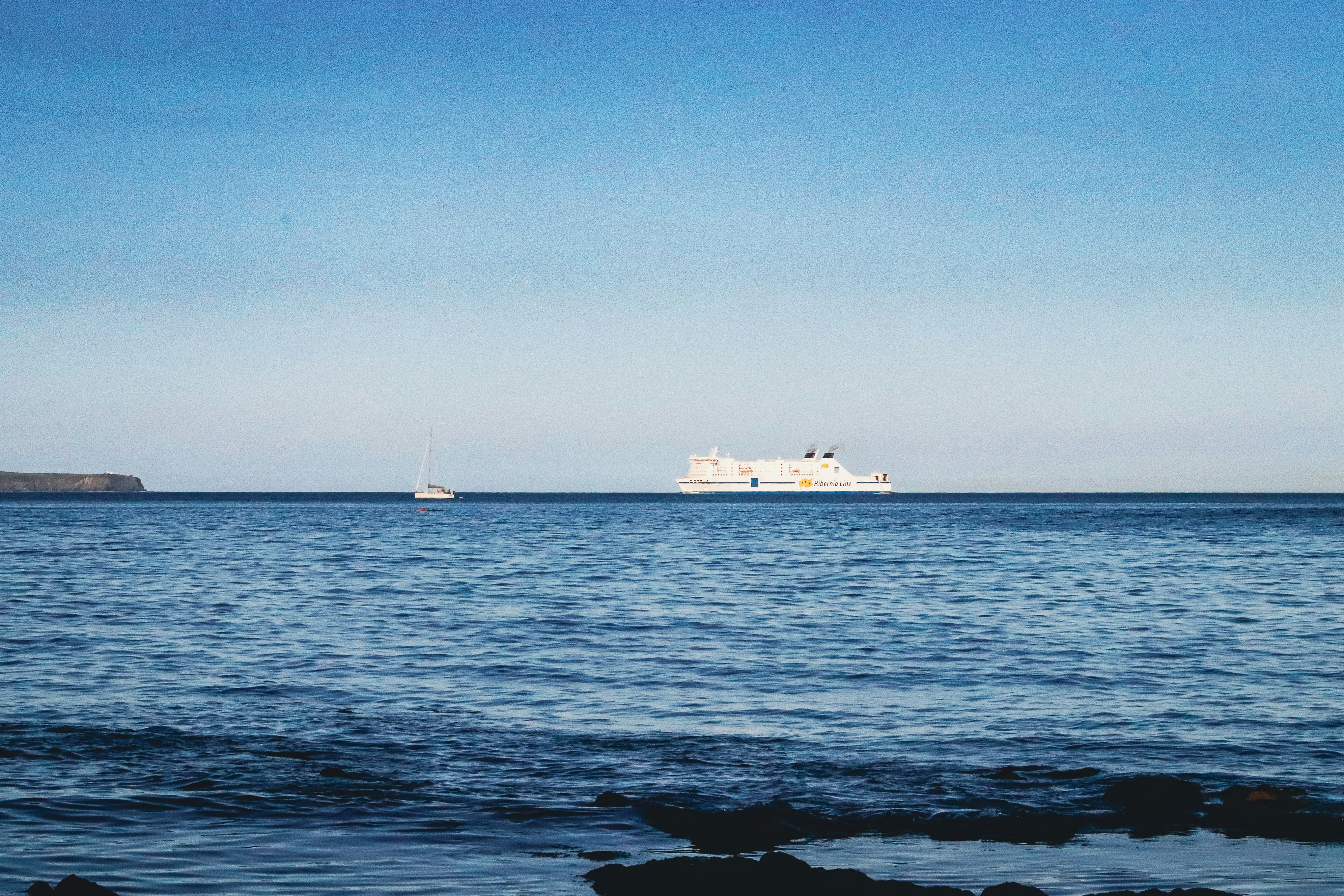 Mid-Sea Passage: A Sailboat and a Cruise Ship on Calm Blue Waters