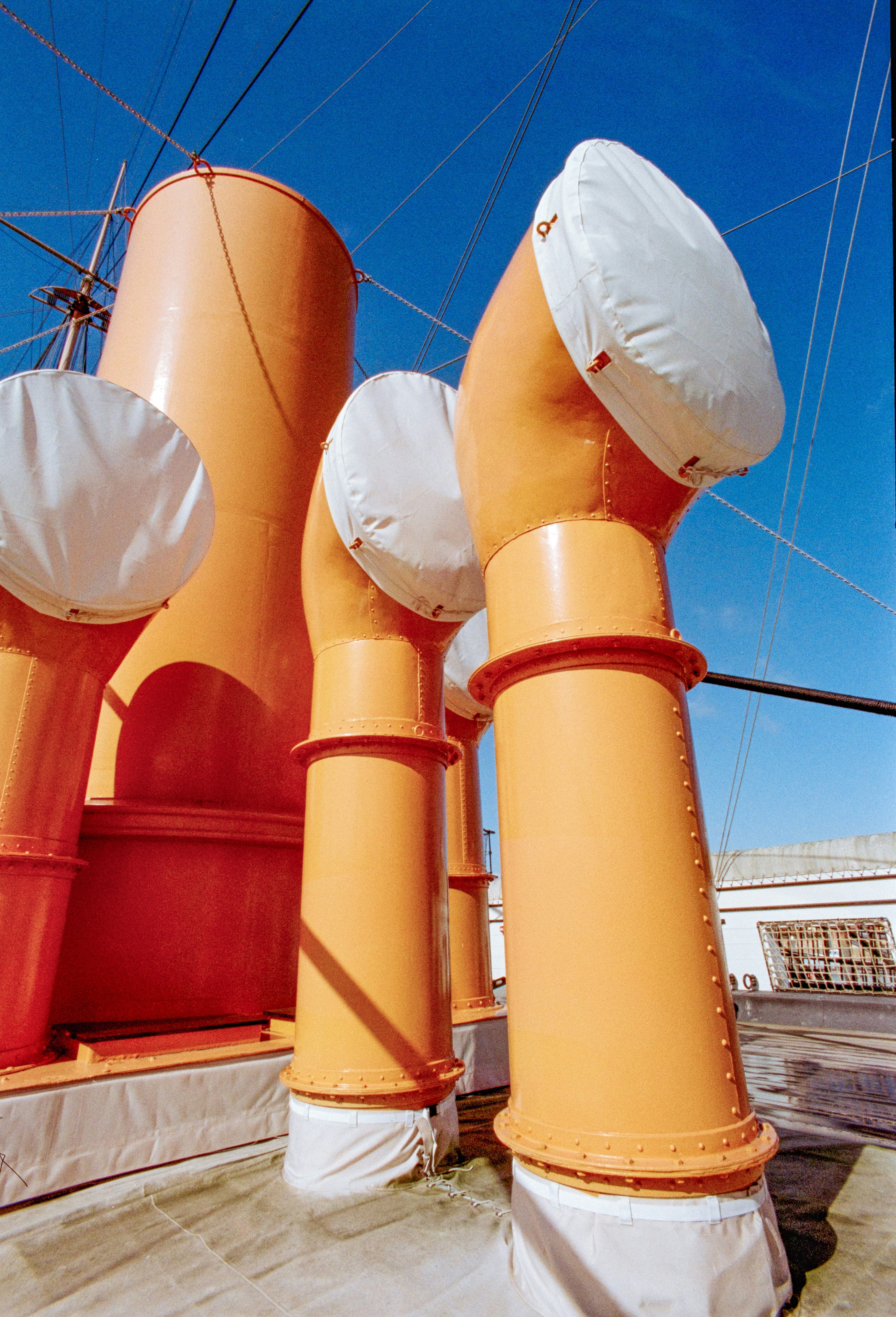 Orange industrial chimneys rise against a vivid blue sky, their white insulated caps catching sunlight as cables cross overhead.