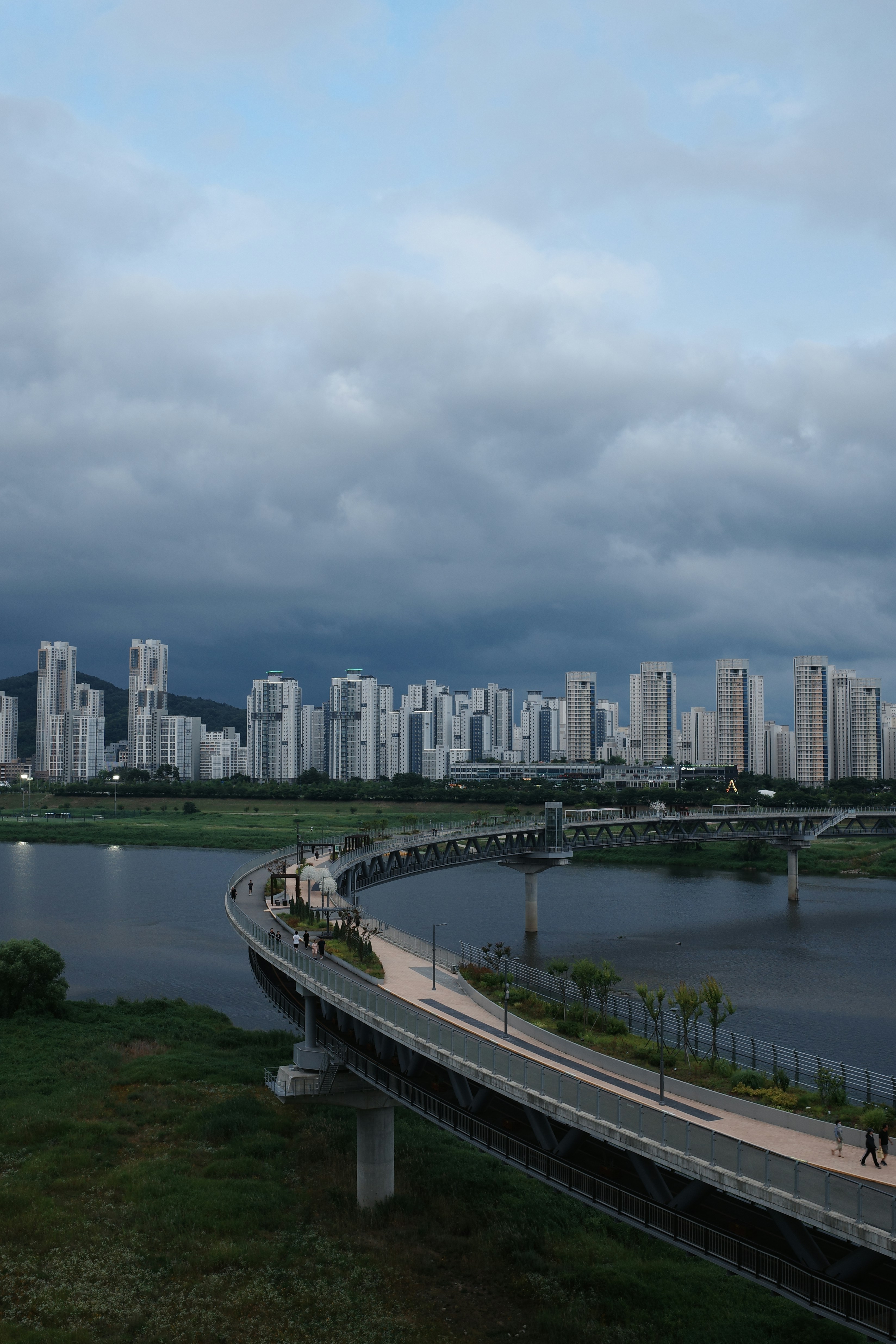 Curved Skytrain Over River: Urban Arc Against a Stormy Horizon