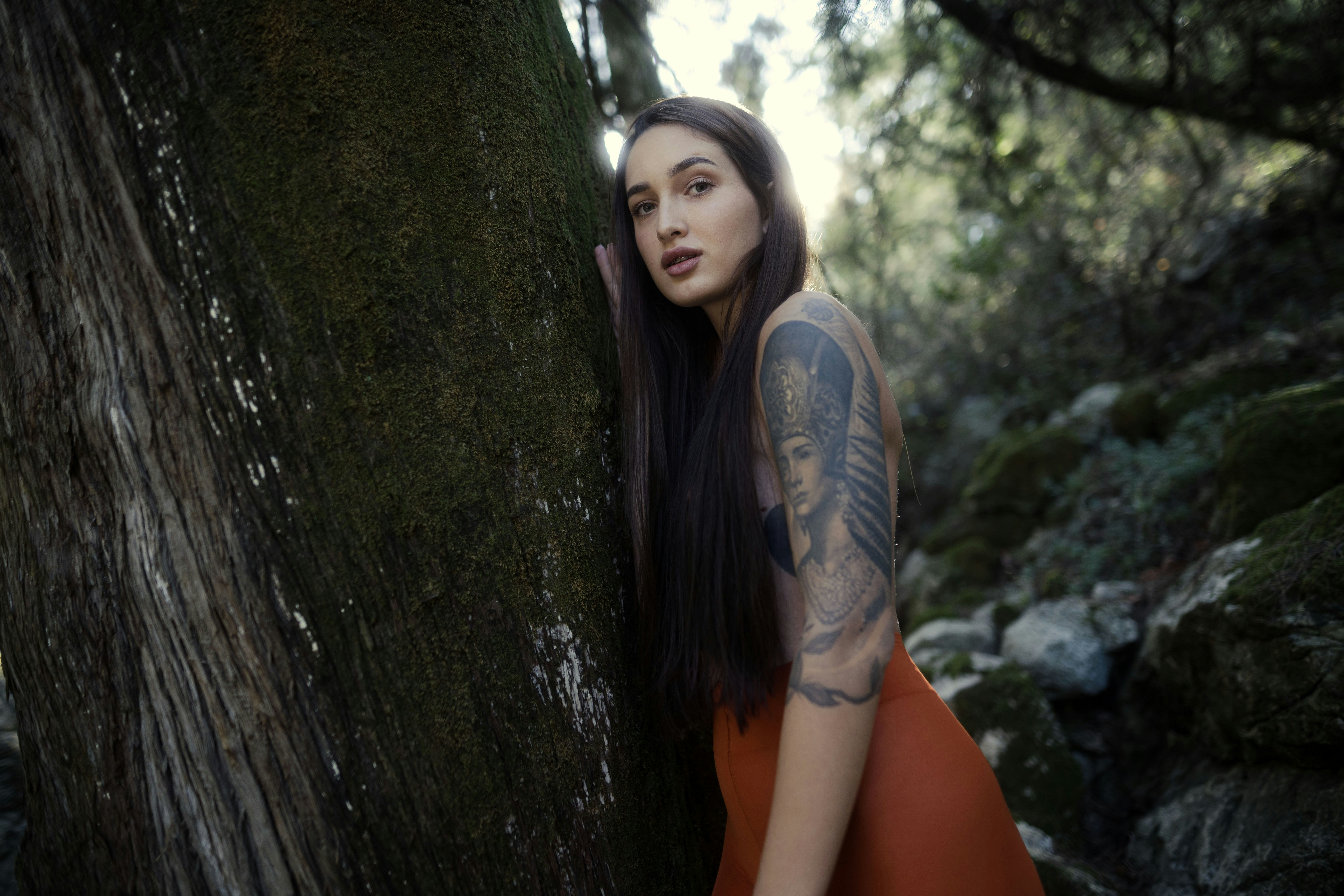 Portrait of Quiet Strength: Woman in Forest with Tattooed Arm against Mossy Tree