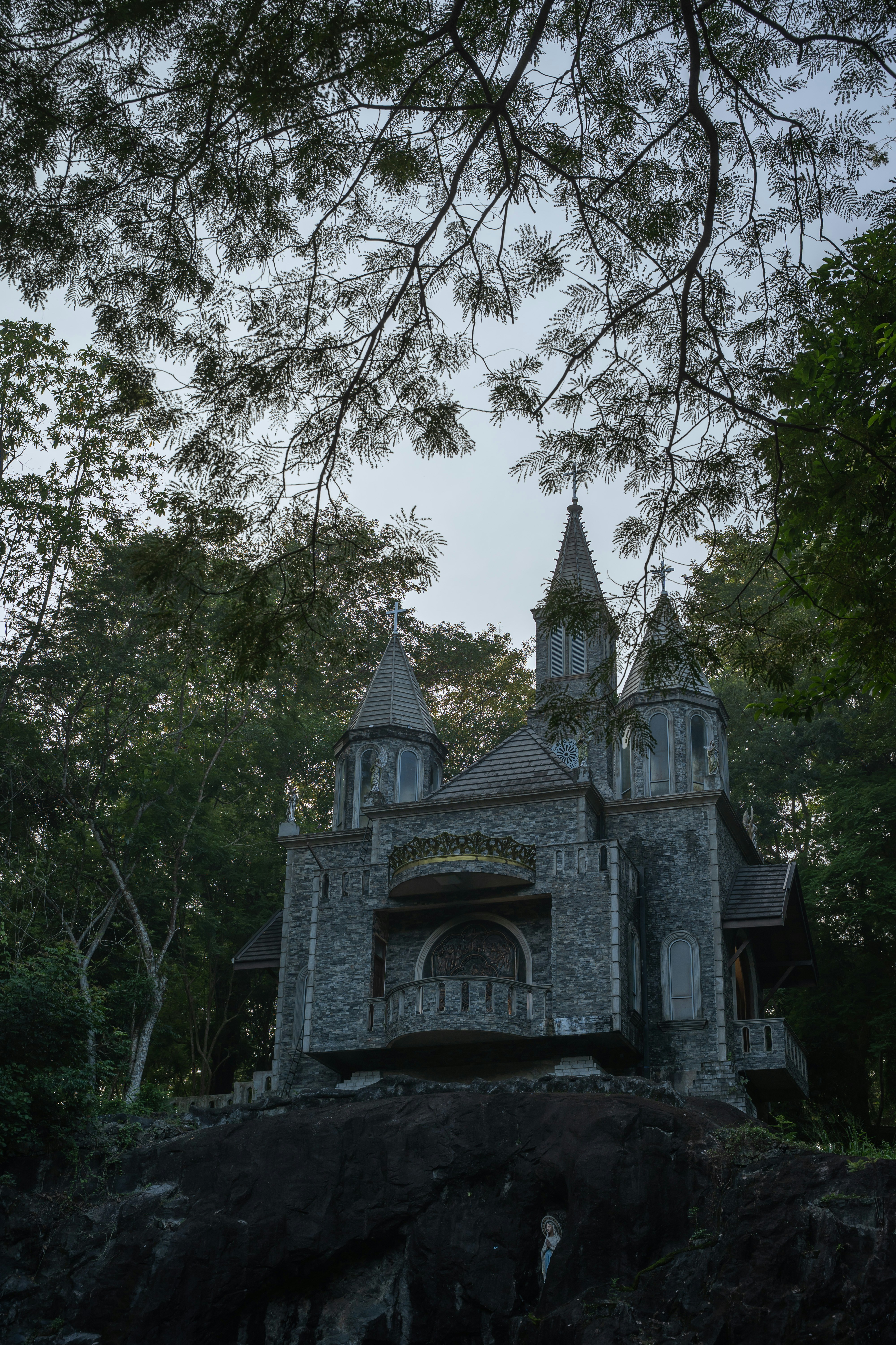 Stone fairy-tale chapel perched on dark basalt, cloaked by trees