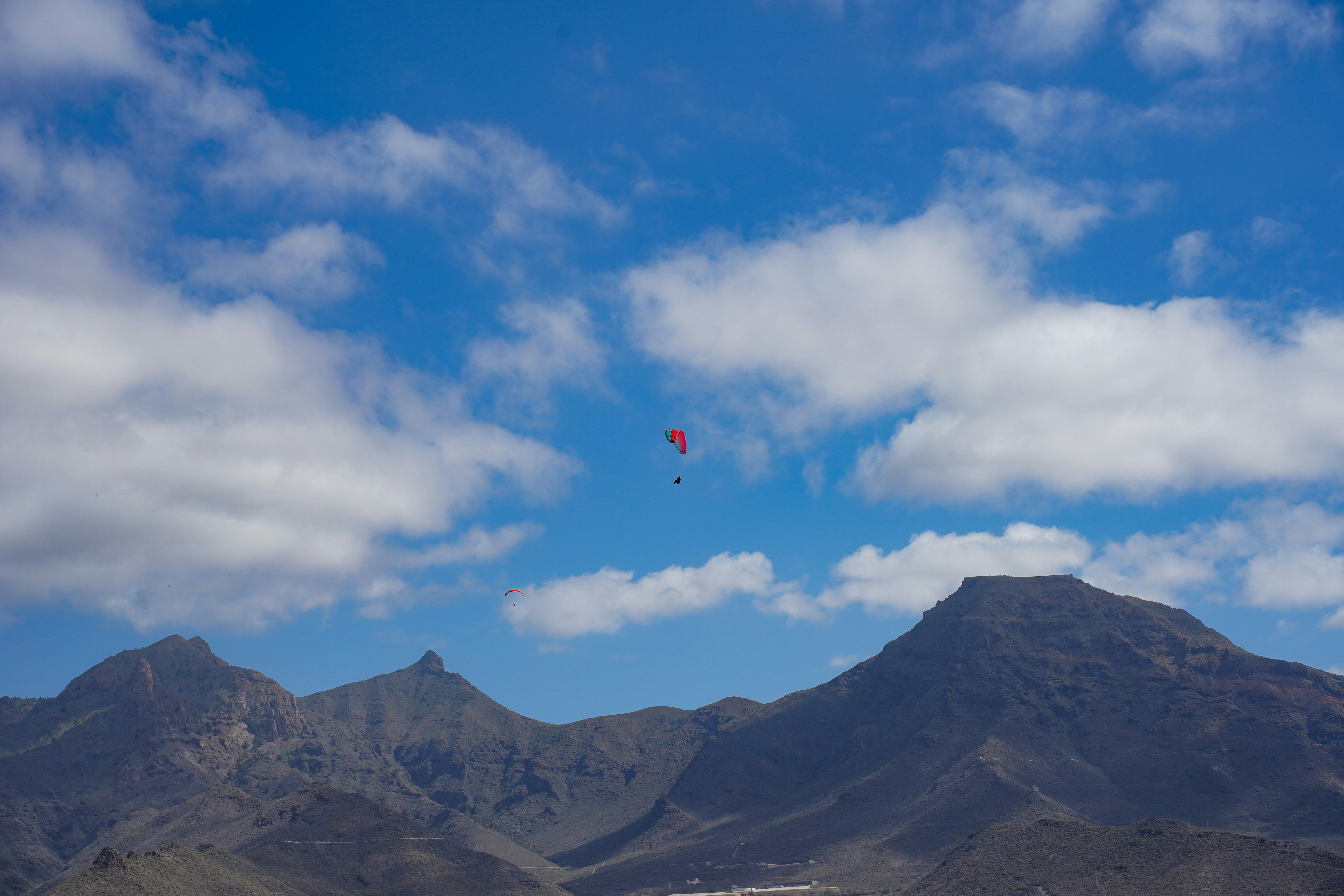 High Altitude Spot: A Tiny Paraglider Drifts Above a Rugged Ridge