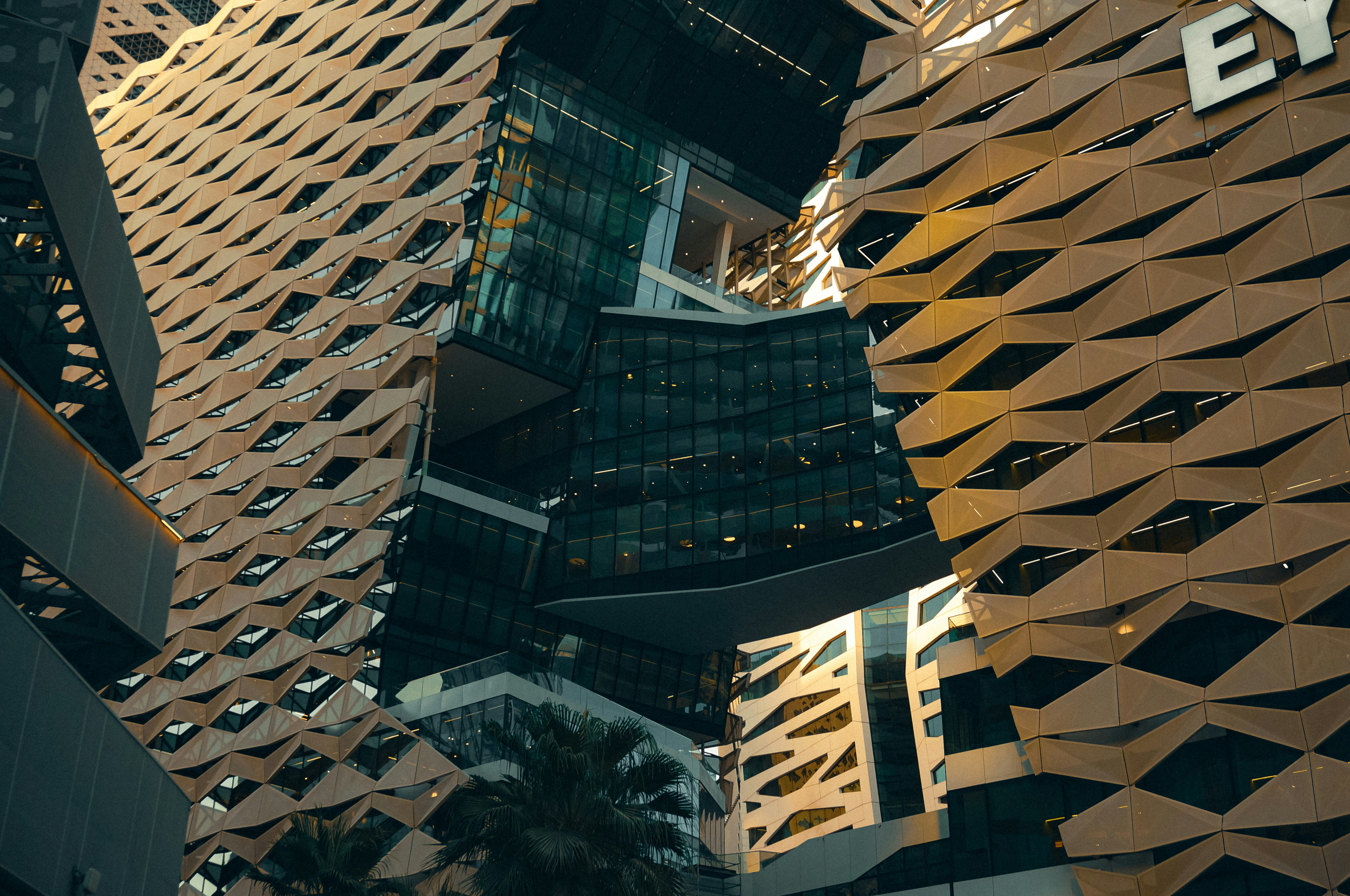 Futuristic architecture with geometric perforated skins and glass skybridge creating negative space between two towers. A moody, low-key urban composition emphasizing texture and contrast.