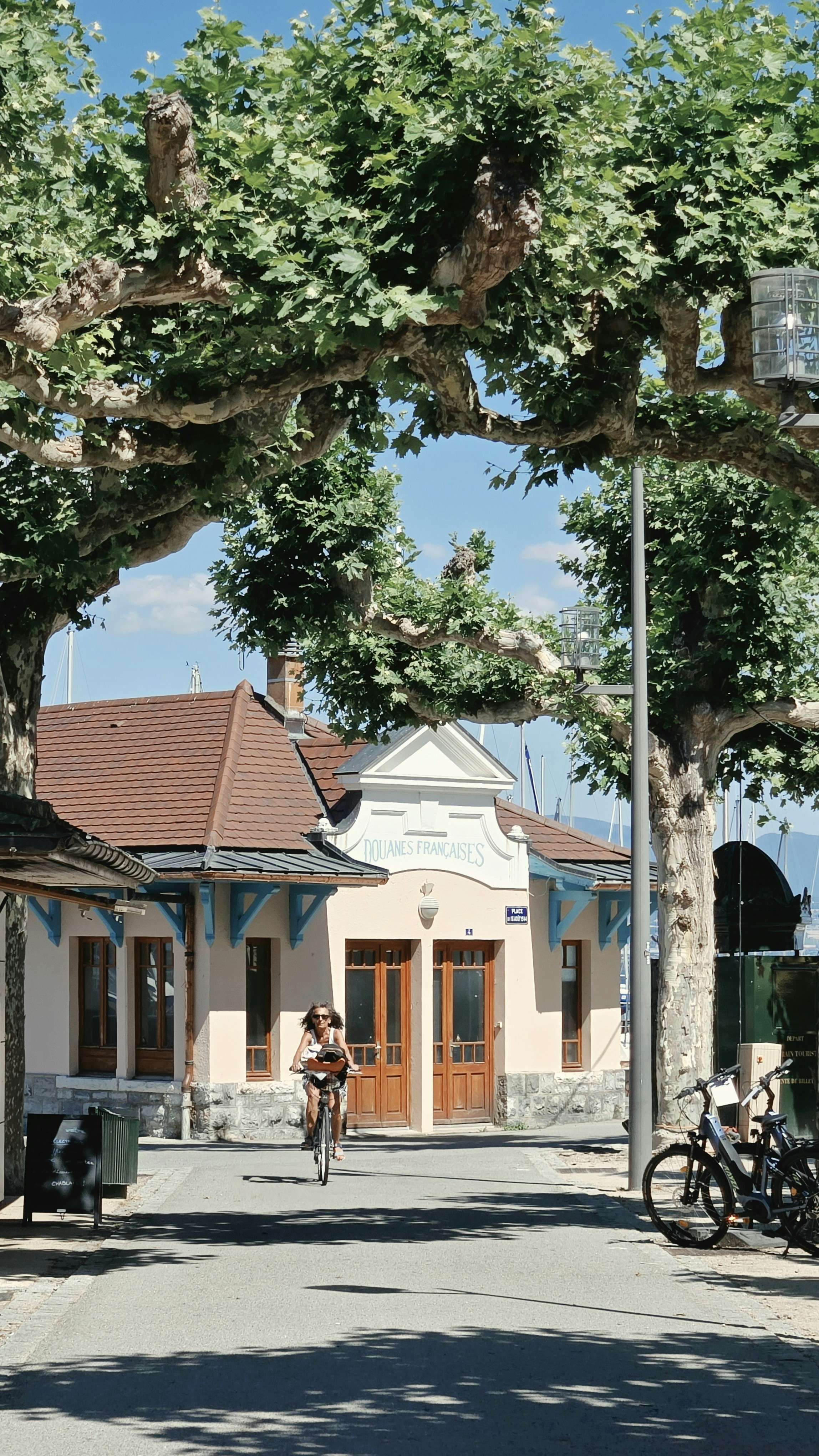 Woman cycling on a tree-lined path past a building.