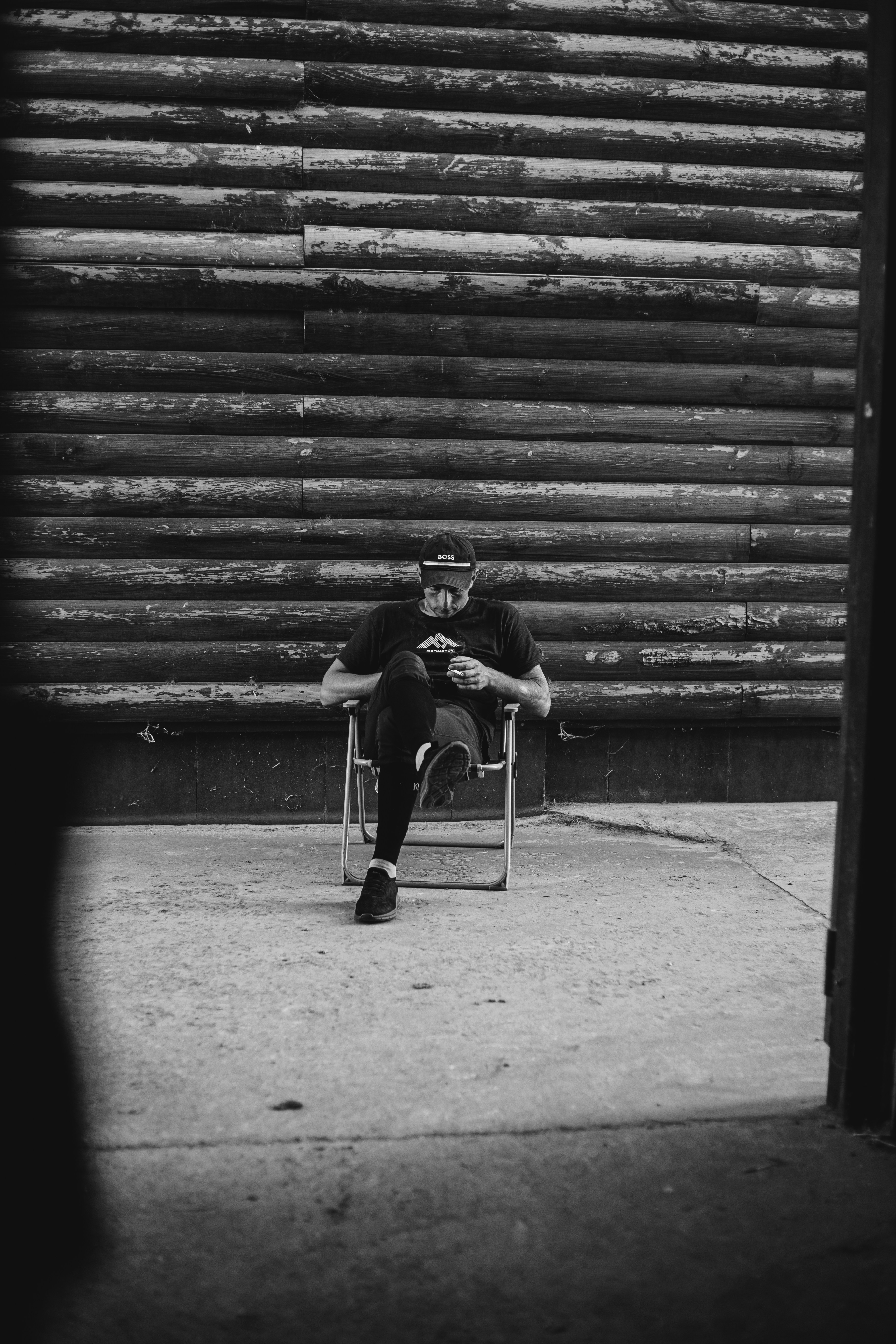 Man in a chair under a weathered wooden wall, absorbed in his phone