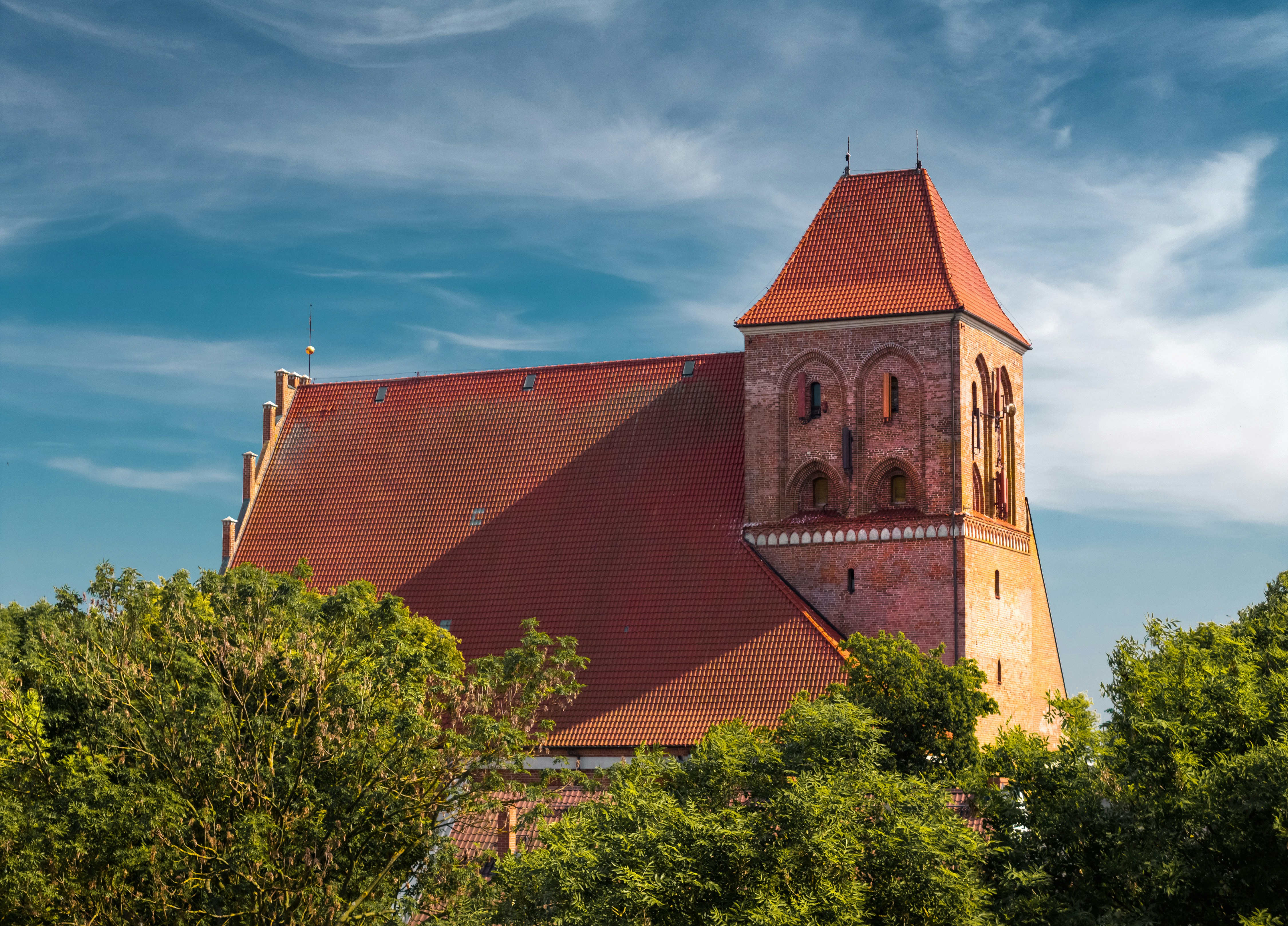 Brick Church Under a Bright Sky: Red Roof and Green Canopy