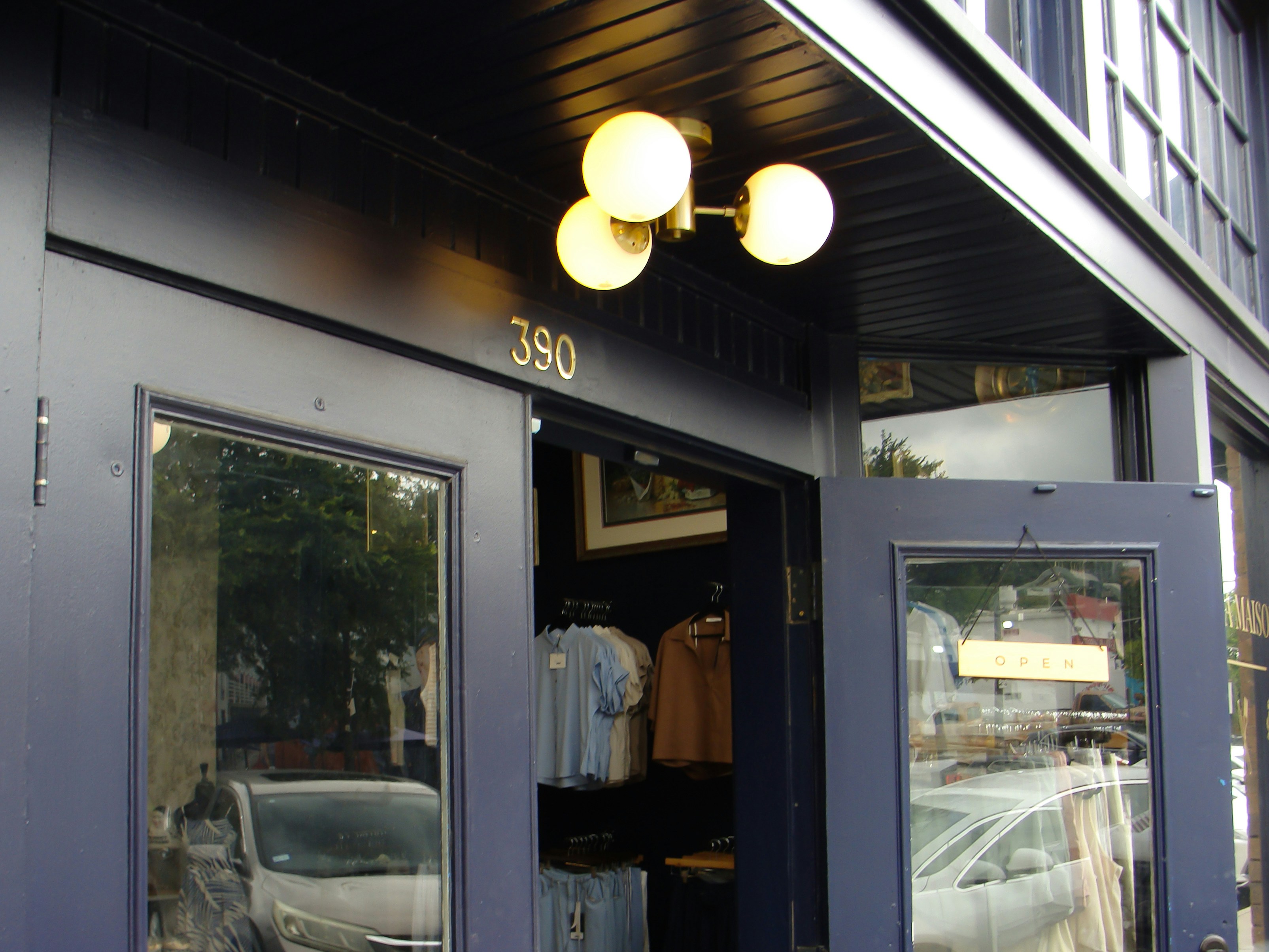 Blue storefront with illuminated globe light above an open door, a car reflected in the glass and clothing inside.