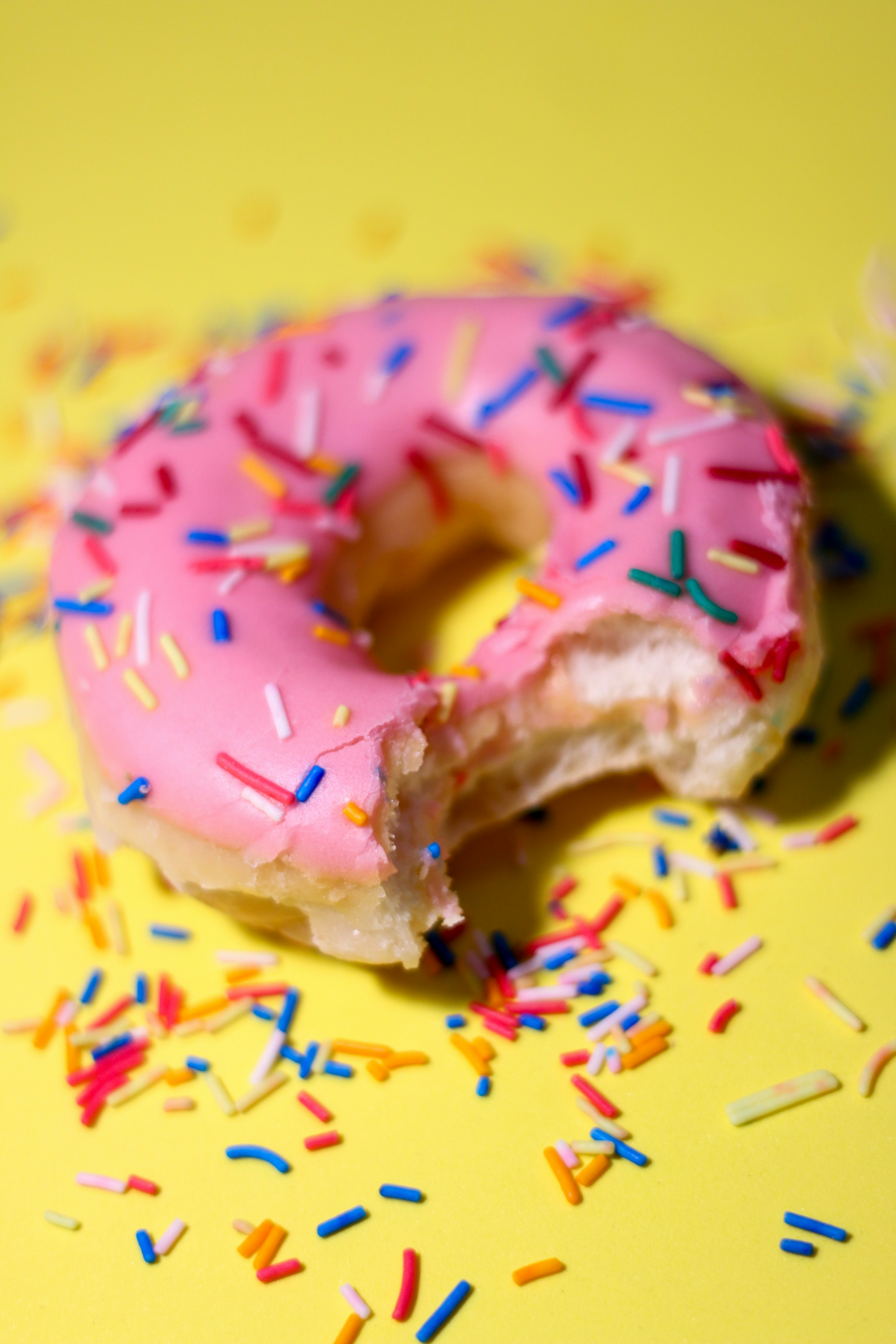 Pink-Glazed Donut with Sprinkles on Bright Yellow Counter