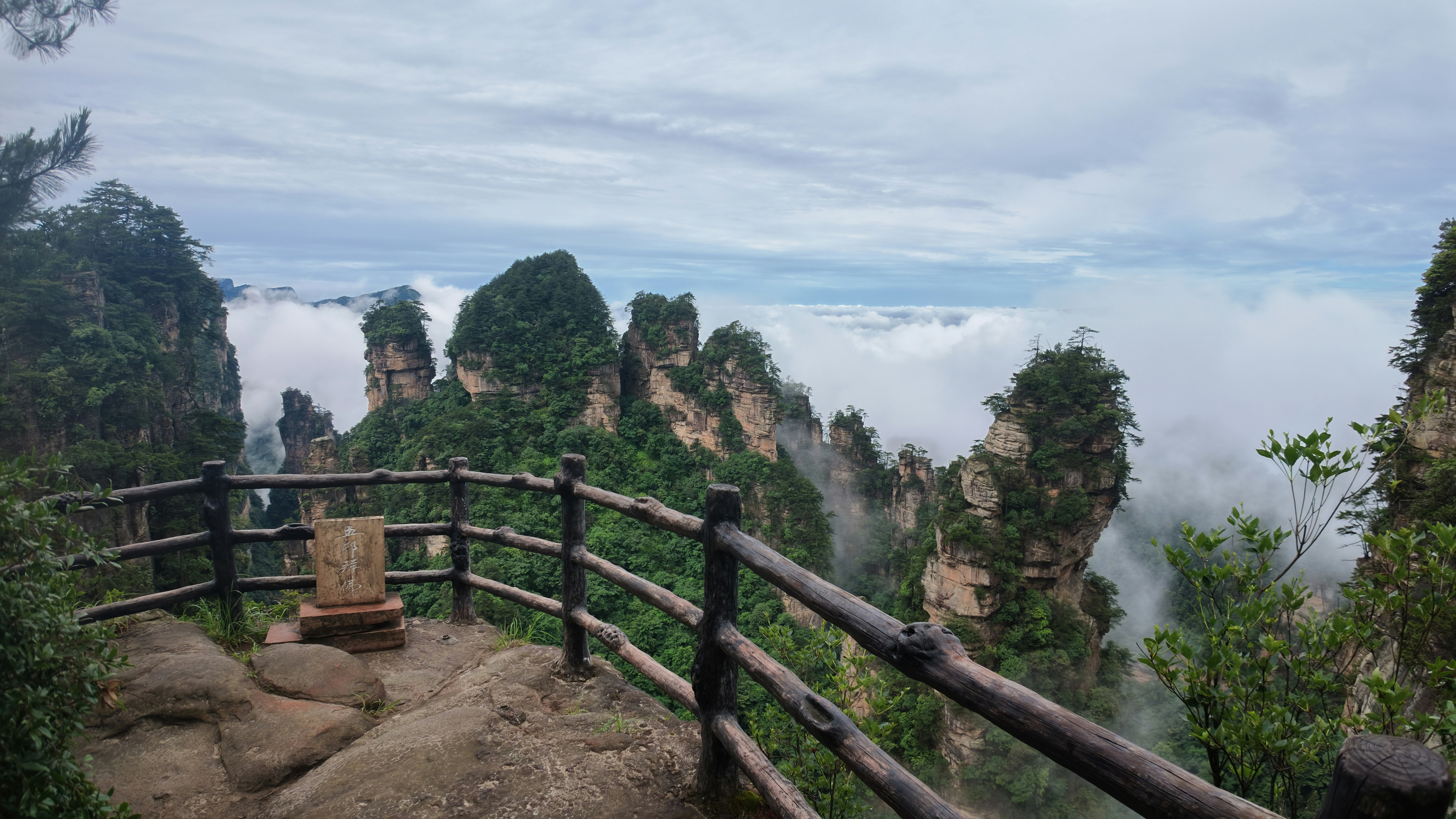 Verdant cliffs rise above a wooden railing trail shrouded in low clouds, conveying a sense of ascent and awe in a high-altitude gorge.