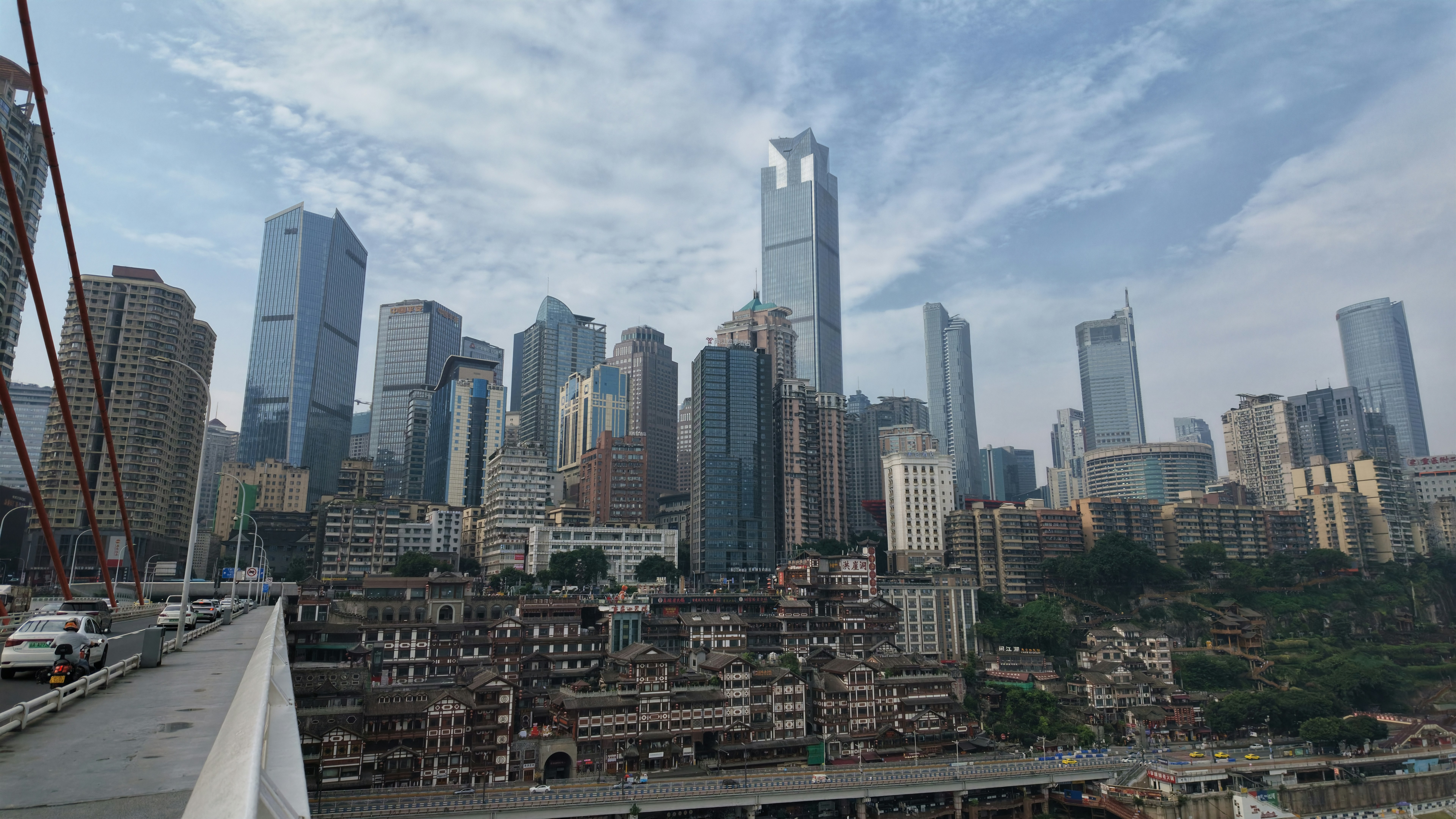 City skyline with a mix of modern high-rises and lower brick buildings beneath a blue sky in daylight. A sweeping urban landscape dominated by glass towers and concrete blocks.