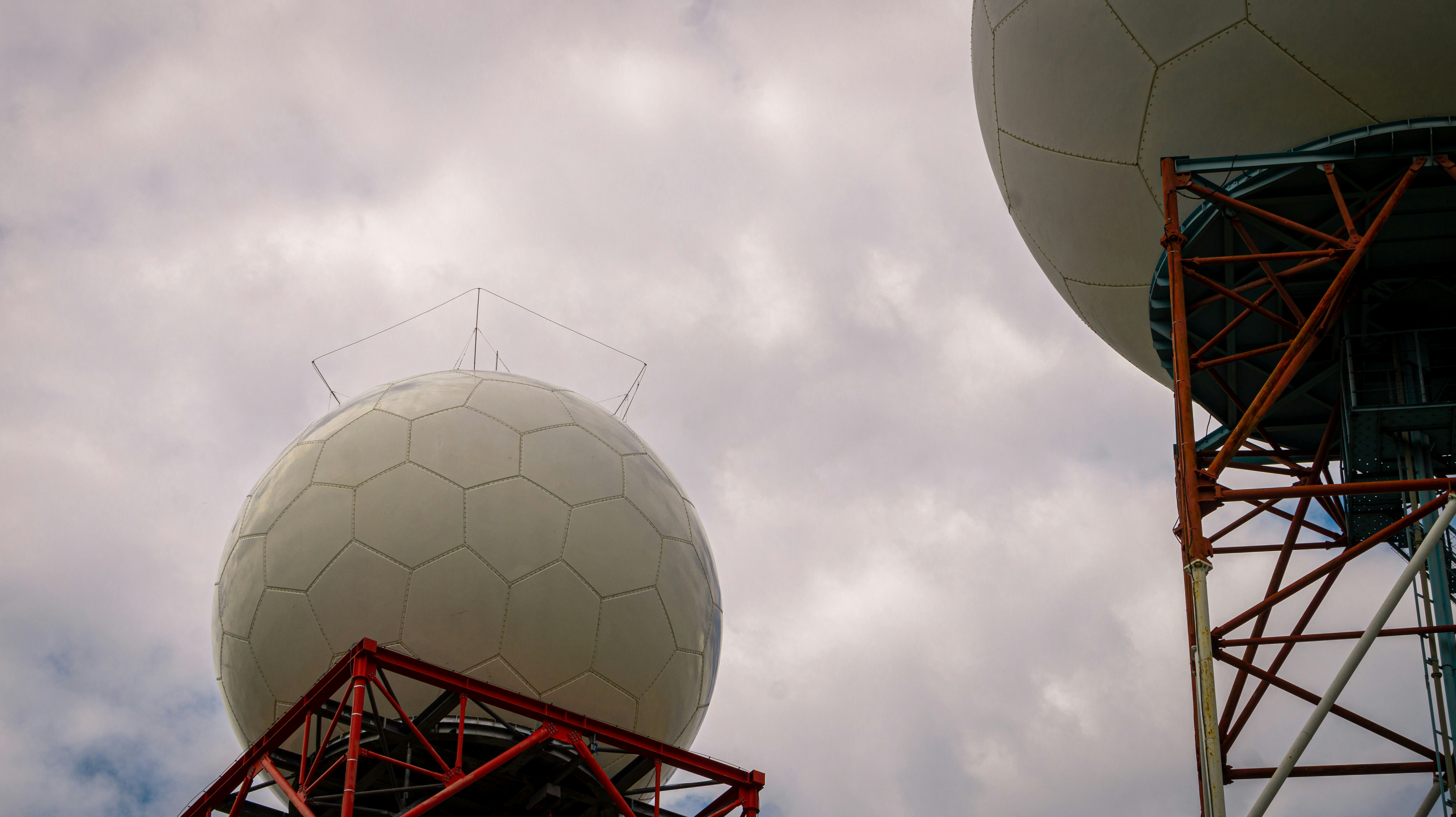 Close-up of large geodesic domes perched on red and white scaffolding under a cloudy sky.