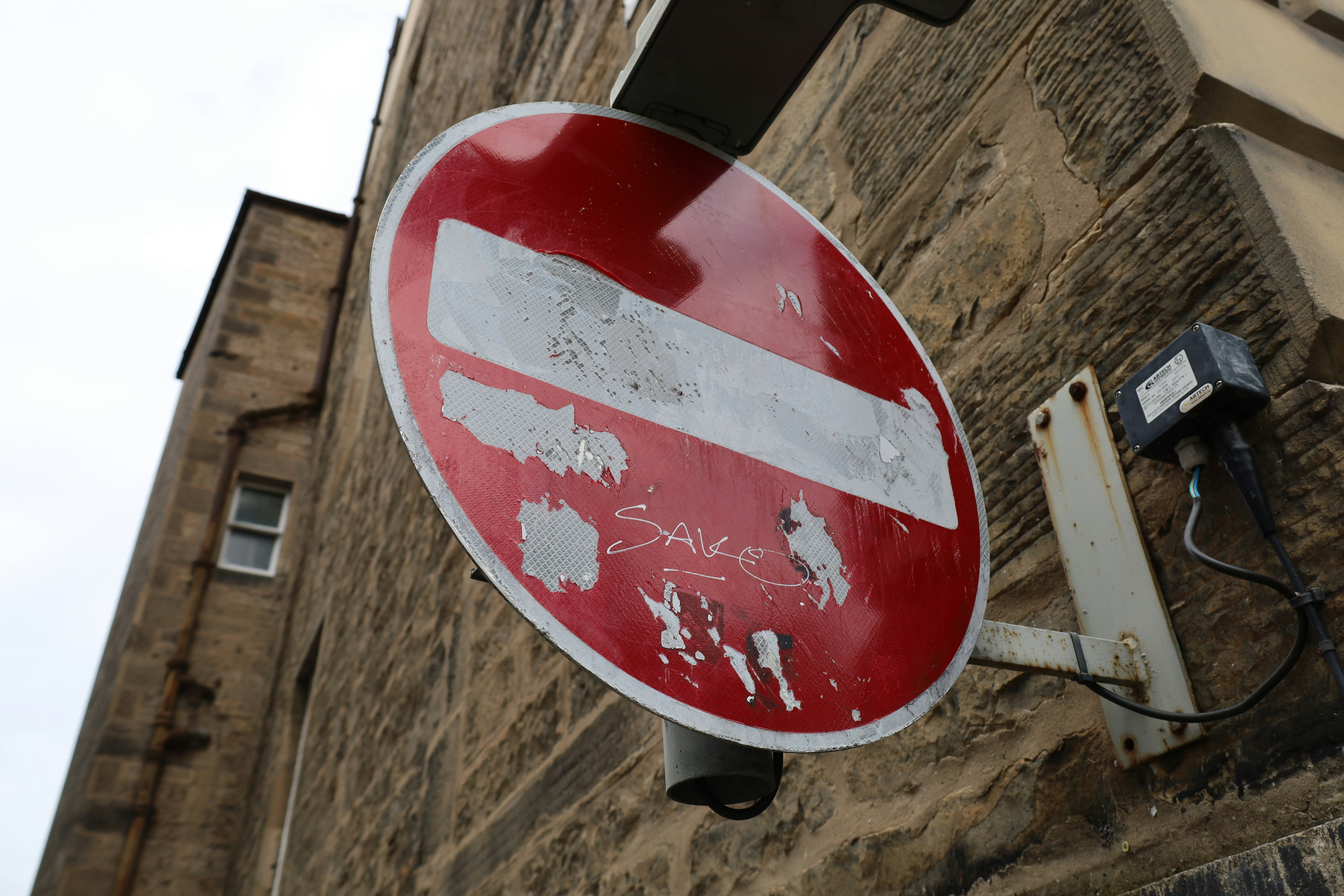 Peeling No-Entry Sign Guarded by Aged Stone Facade