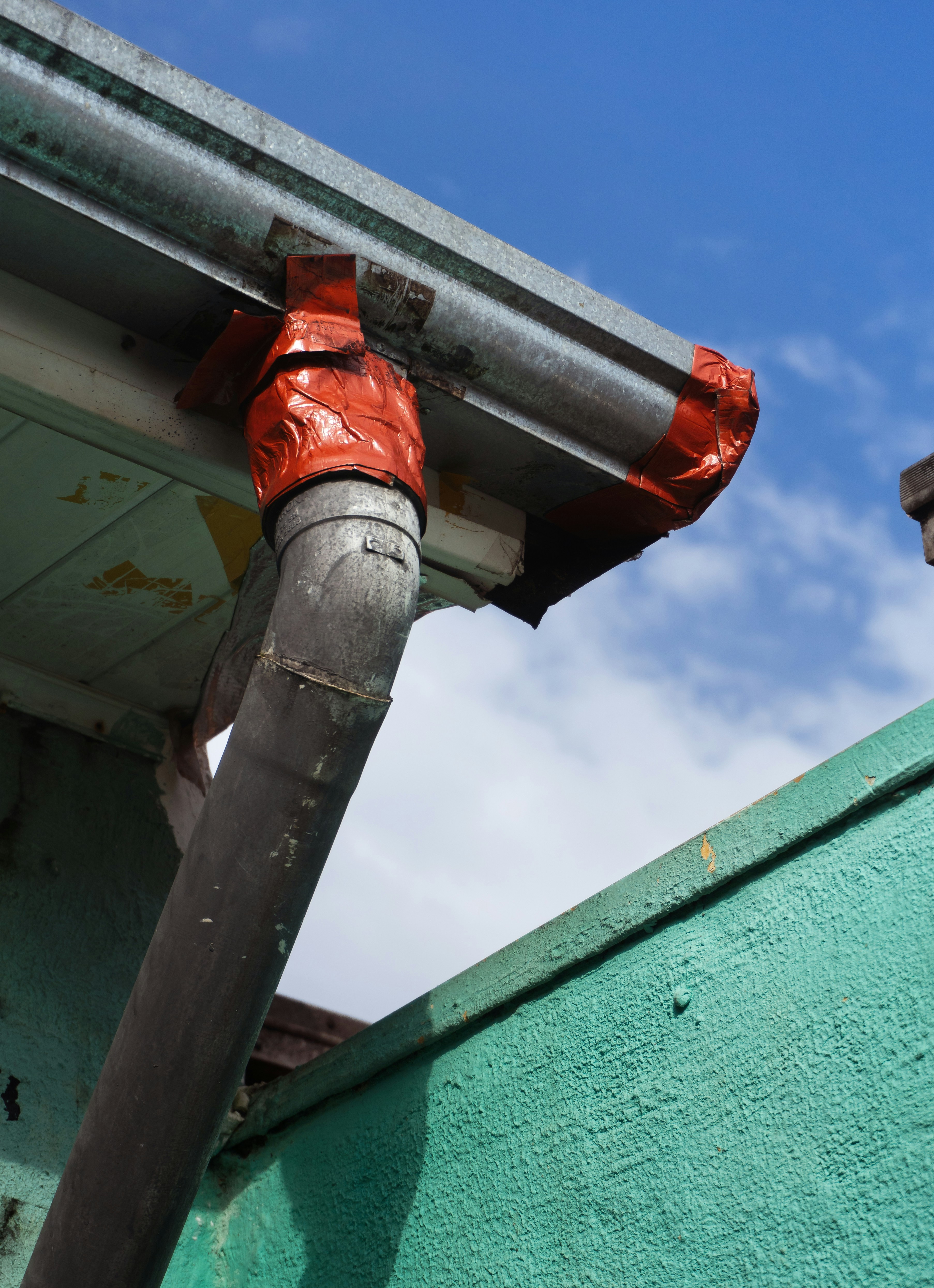 Red Tape and Rain Gutter: Corner of a Weathered Roof