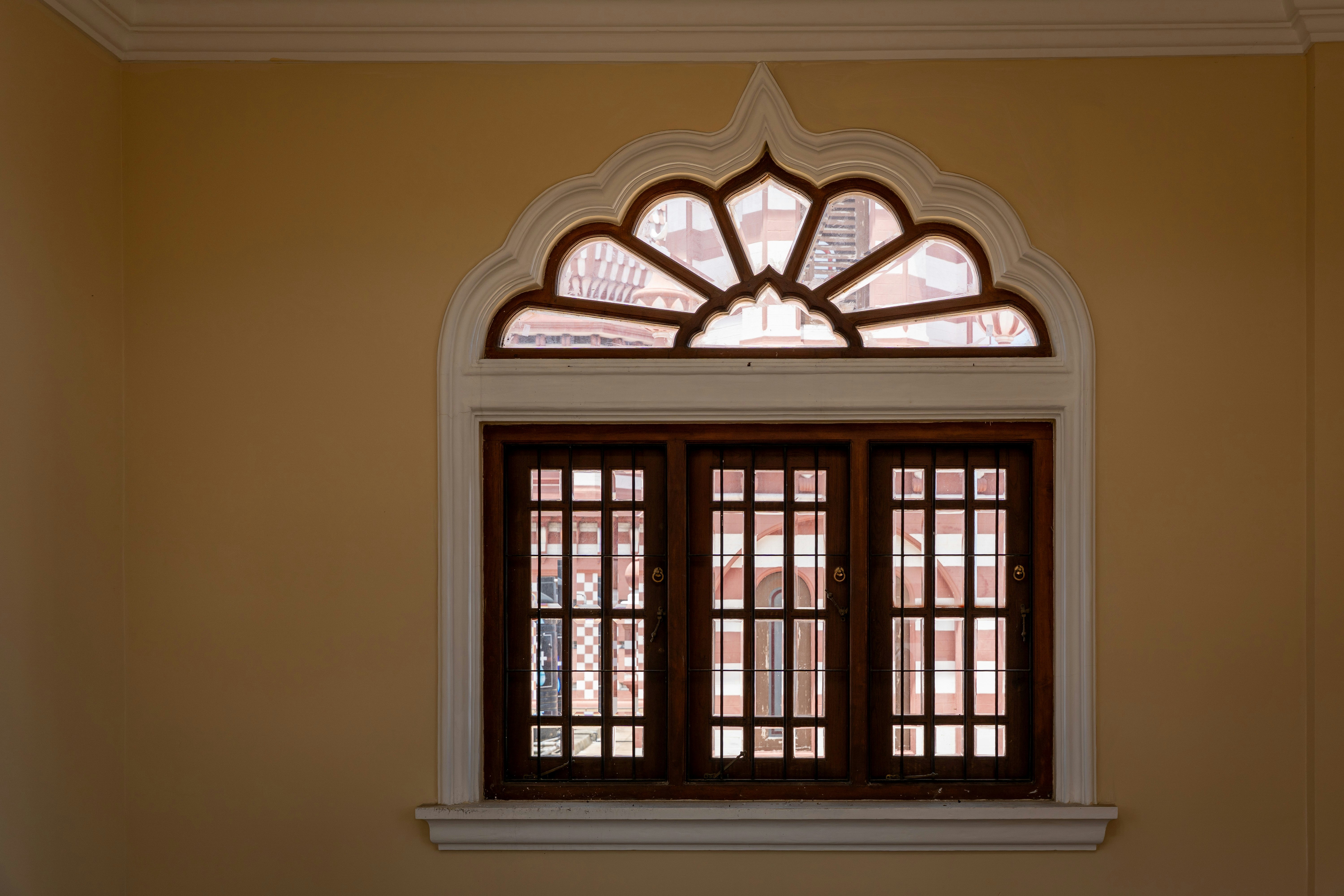 Arched window with decorative grille framed by warm yellow wall