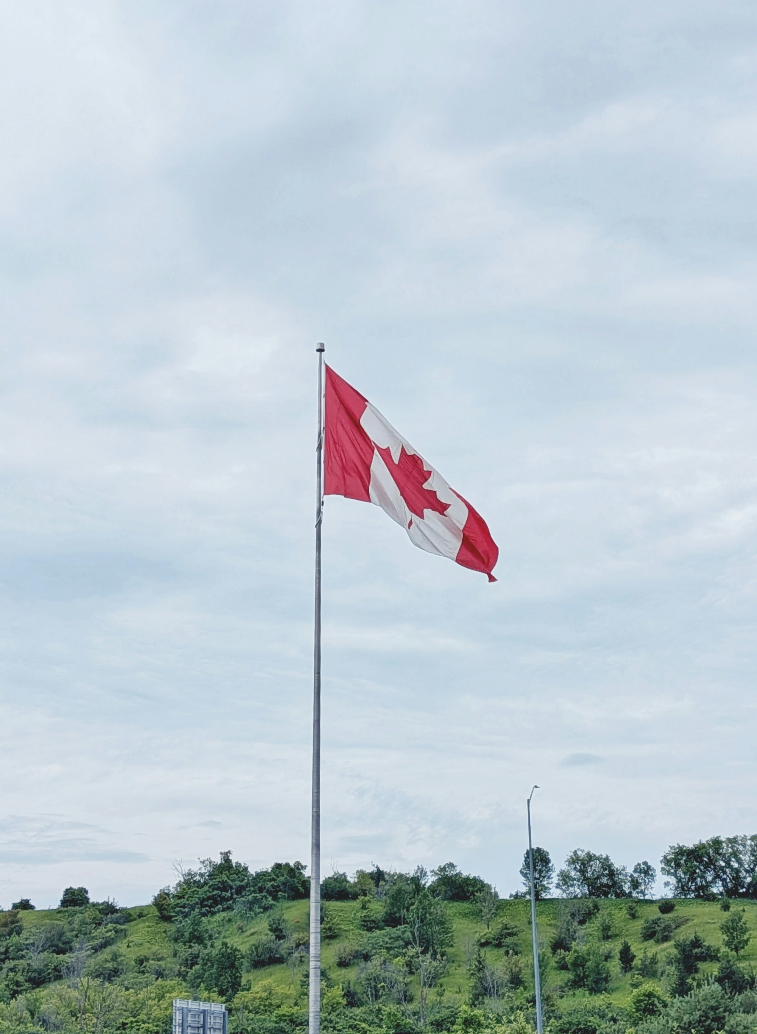 Flag over gentle hillside: Canada’s emblem against an open sky