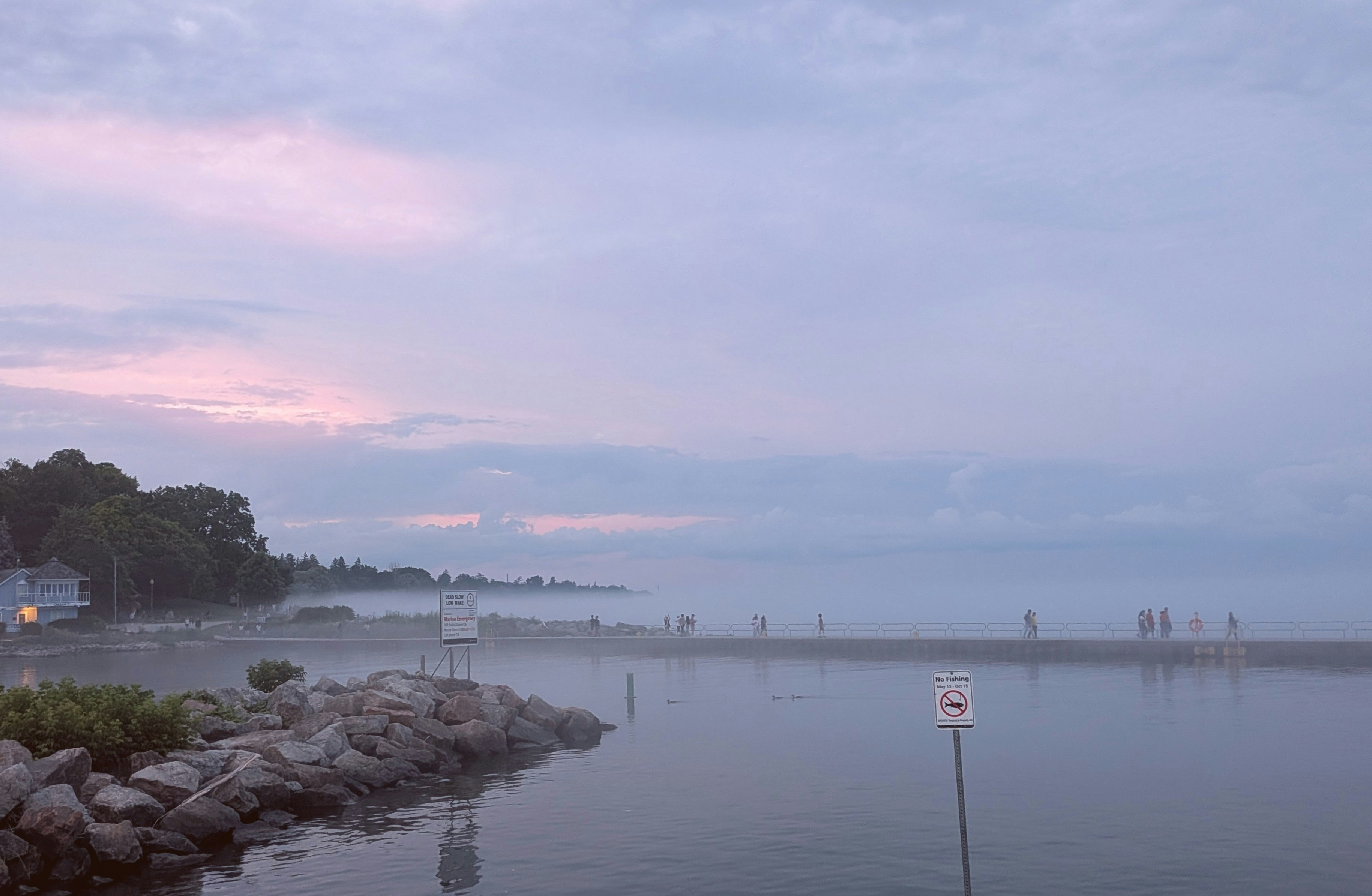 Soft Dawn Over a Calm Lake: Distant Silhouettes at the Breakwater