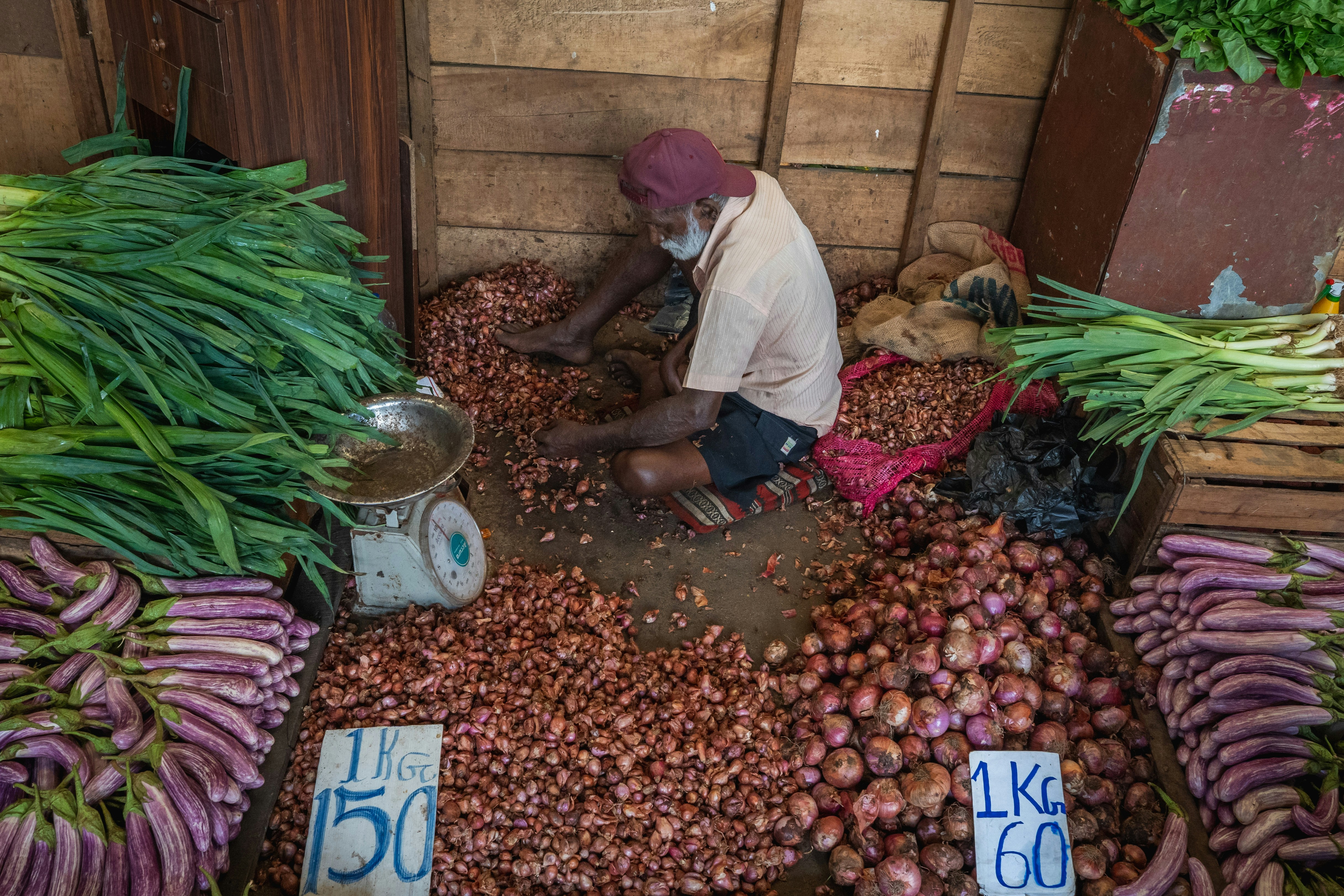 Vendor Sorting Red Onions in a Market Alley