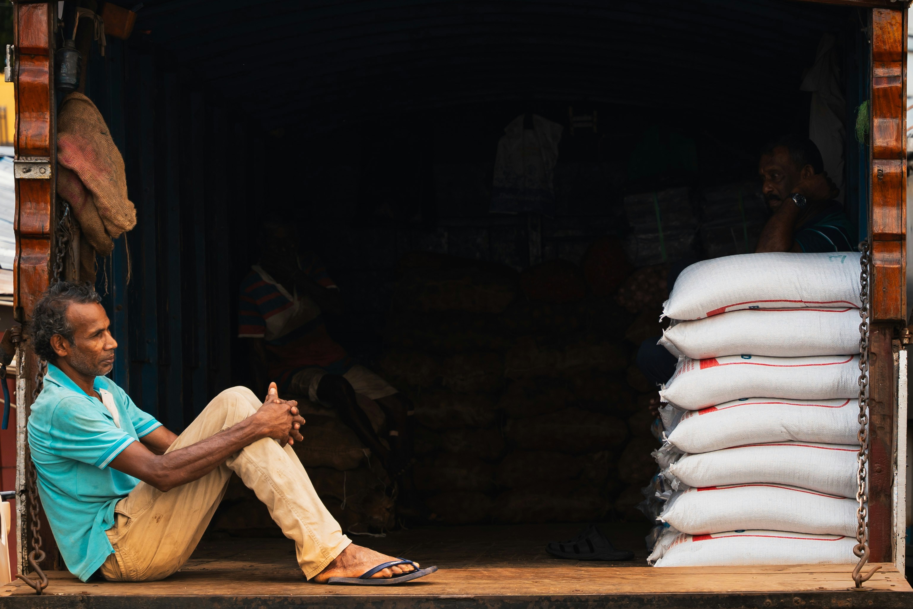 Quiet Exit: A Man Seated in a Sack-Stacked Dock Interior