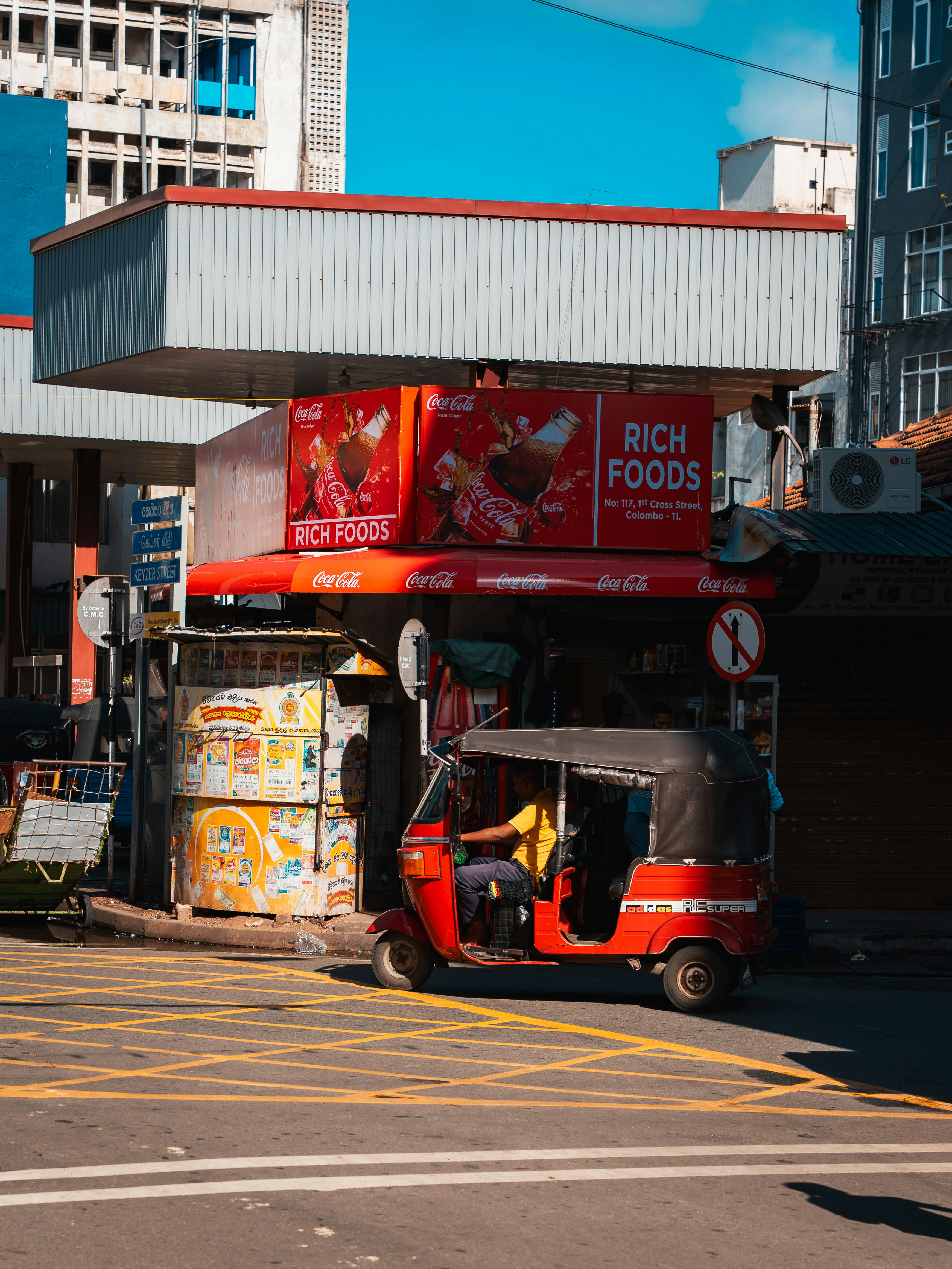 Streetfront Convenience: A Red Auto Rickshaw Near a Coca-Cola Rich Foods Stand